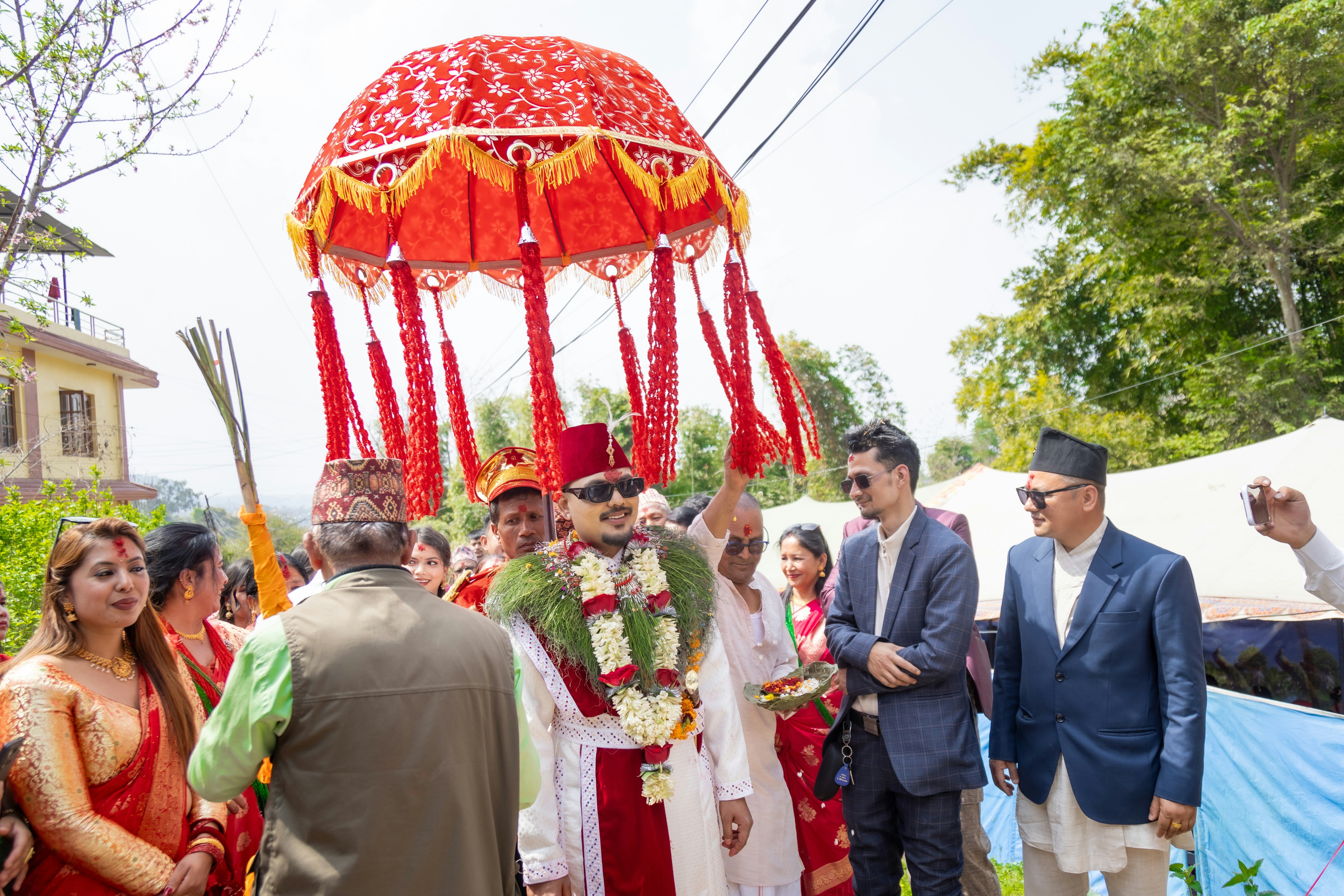 A festive groom under a vibrant ceremonial parasol surrounded by joyful guests