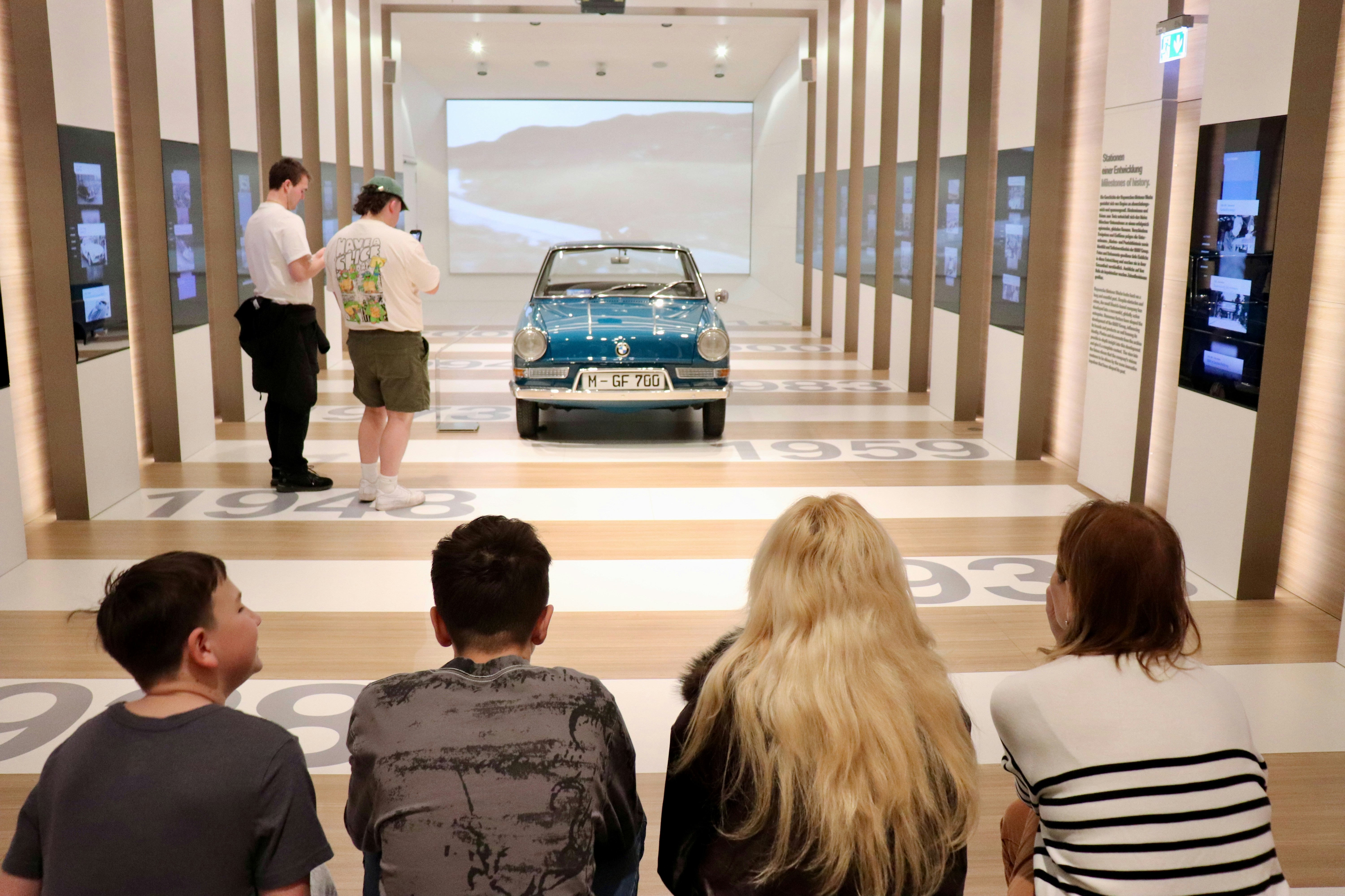 Blue vintage car on a pedestal framed by observers in a modern gallery