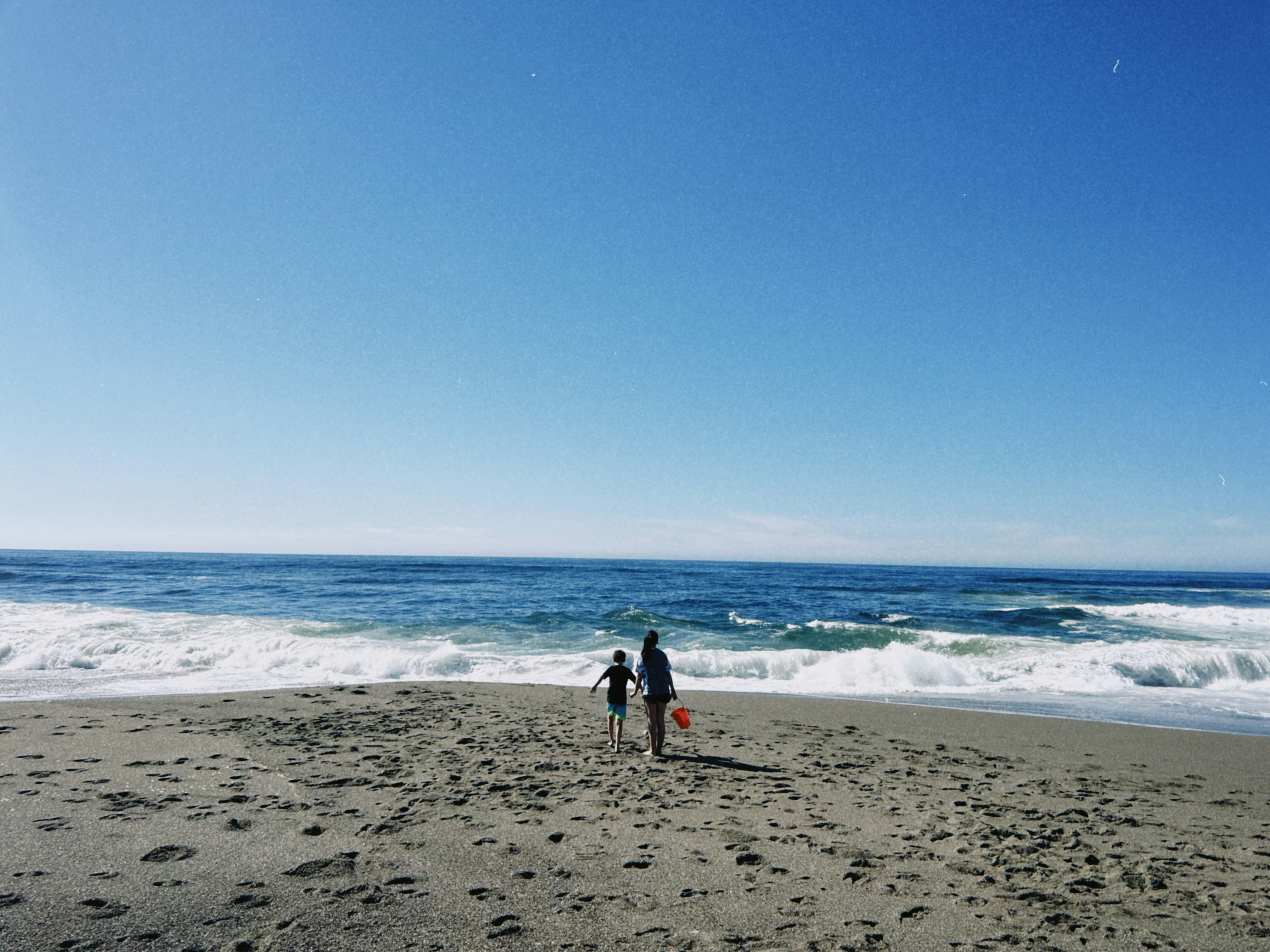 Two hikers on a sunlit beach move toward the breaking waves