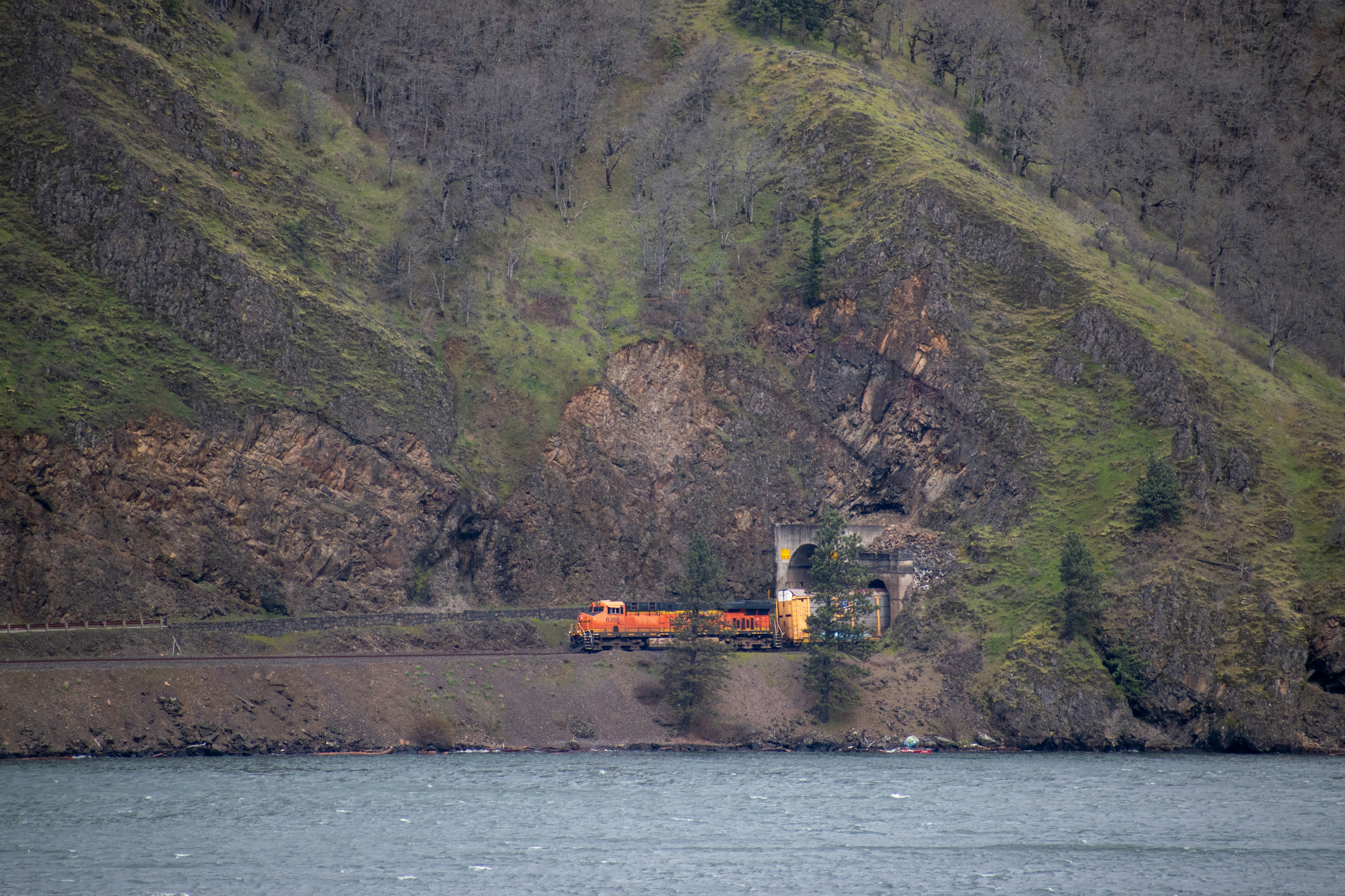 Orange locomotive emerging from hillside tunnel along rugged shoreline