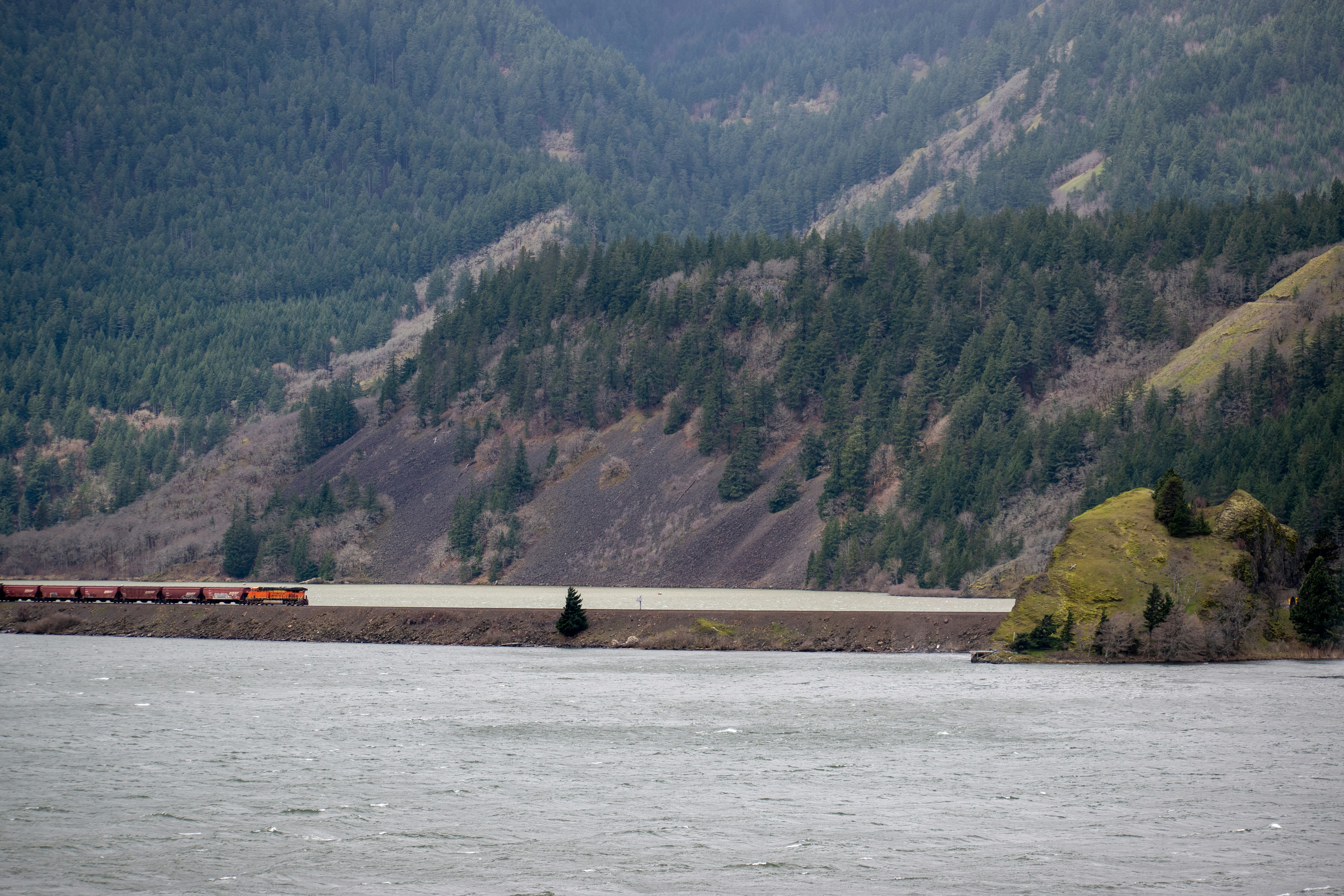 Railcar on a distant shoreline beneath forested hills