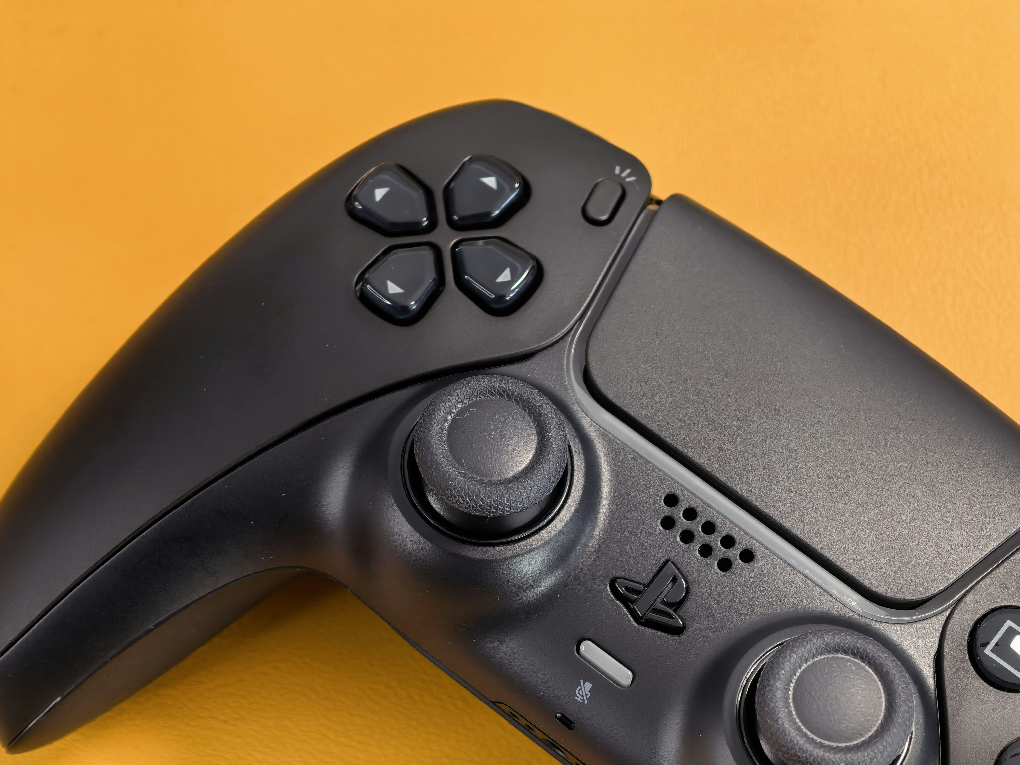 Close-up of a black wireless game controller's right-hand grip and face buttons against a warm orange surface.