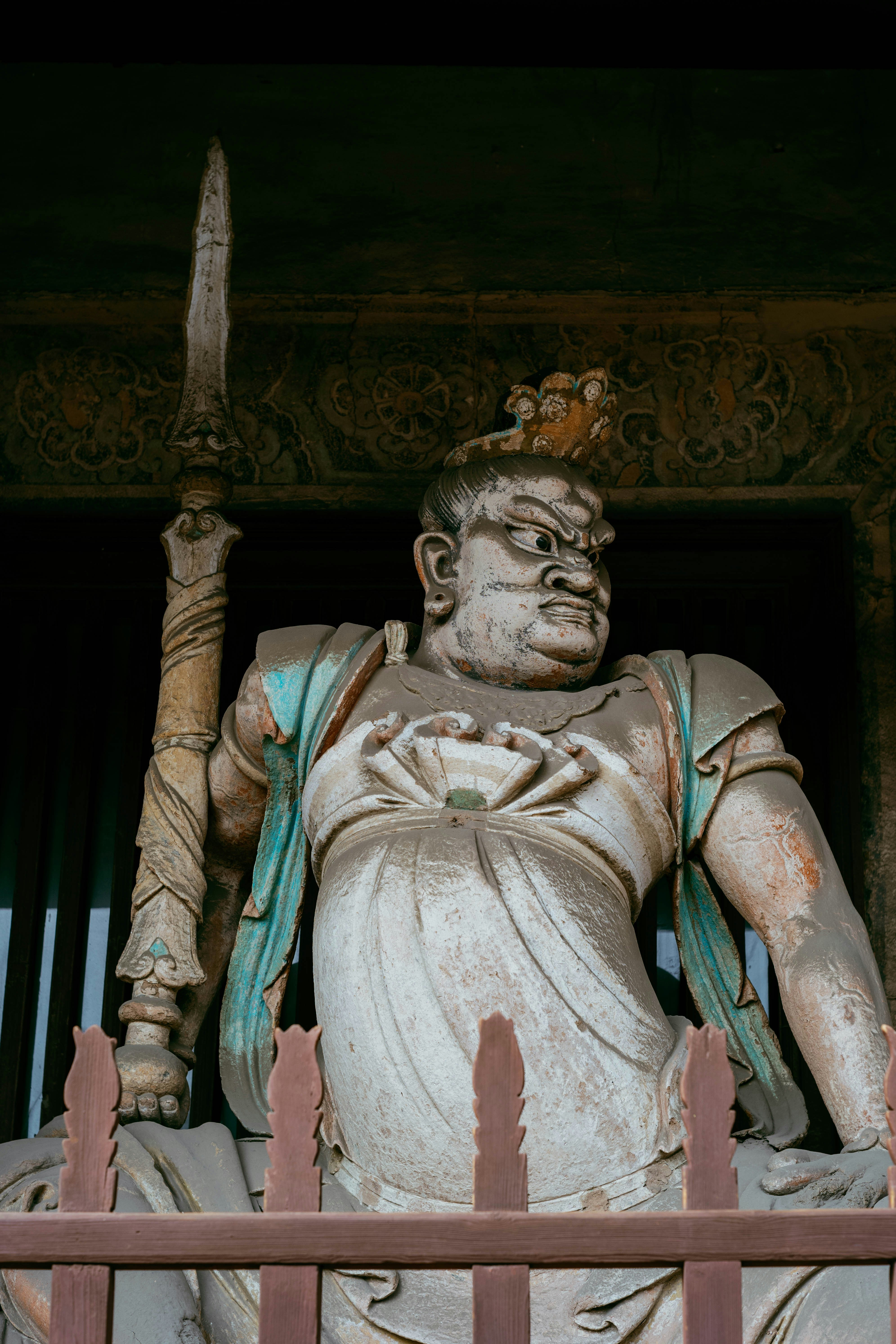 Stoic guardian: weathered deity with raised blade under dim shrine light
