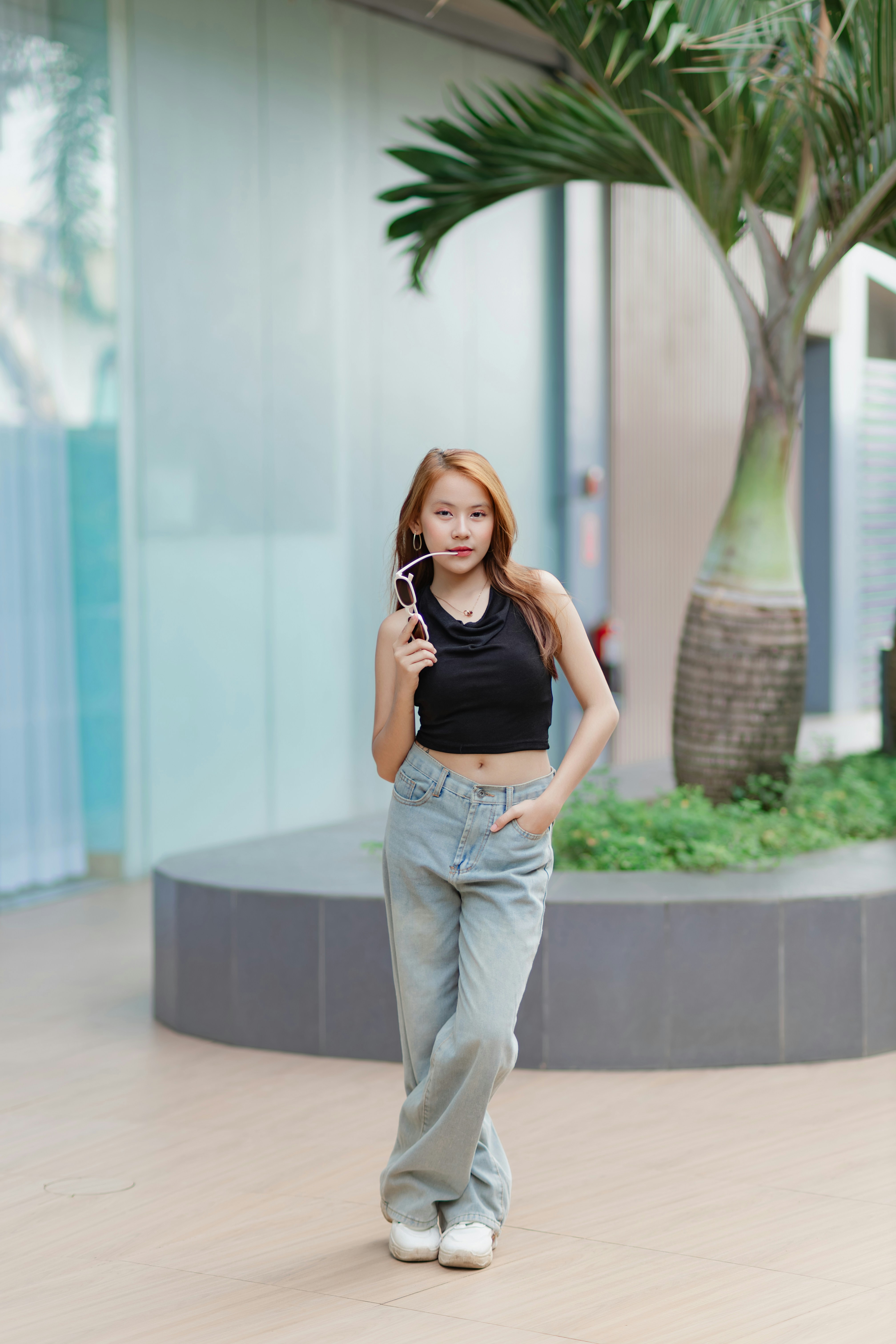 Casual Confidence: A Young Woman with Sunglasses by a Plant-Filled Courtyard