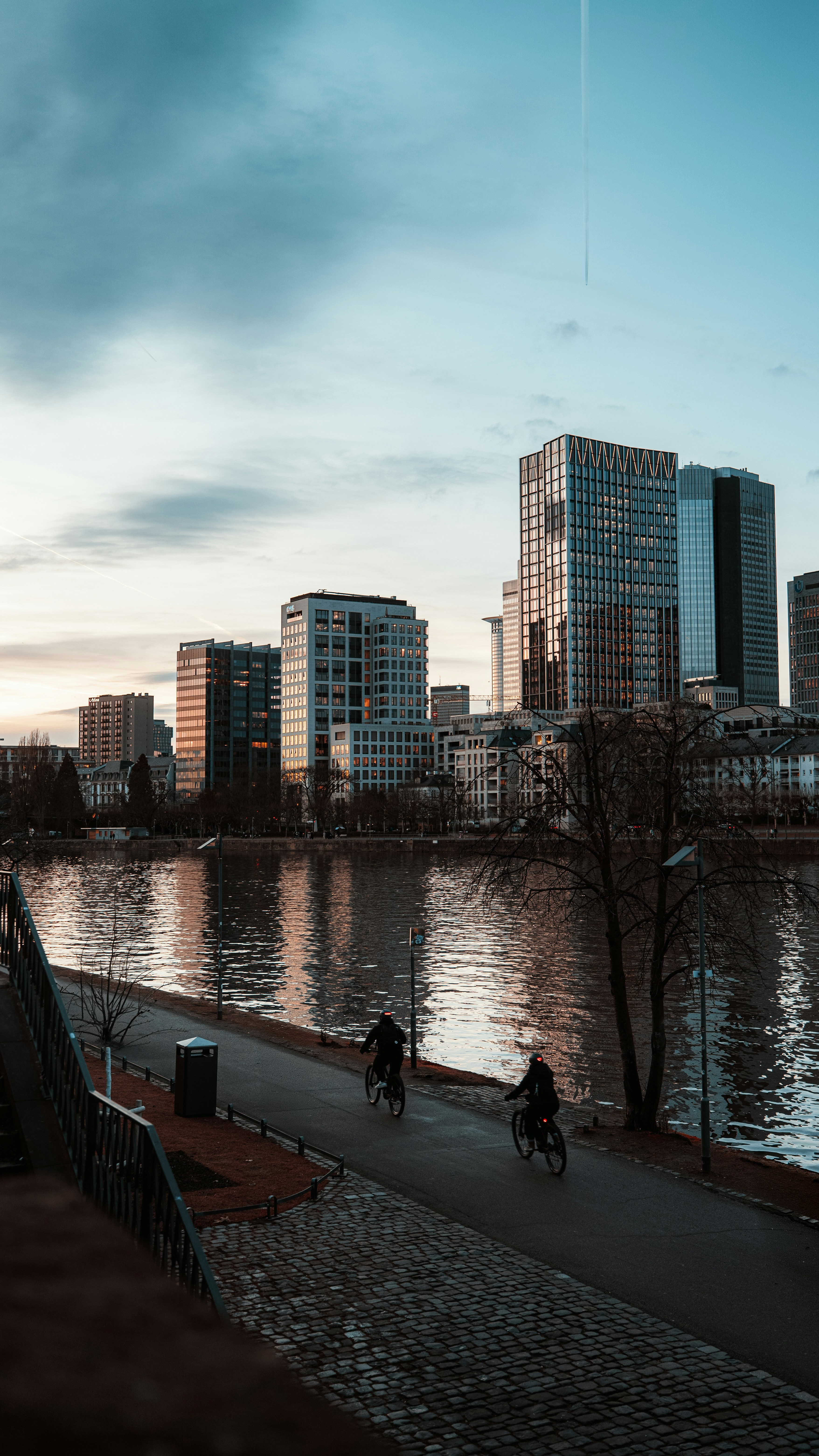 Riverside Skyline at Dusk: Bikers in the Quiet Promenade