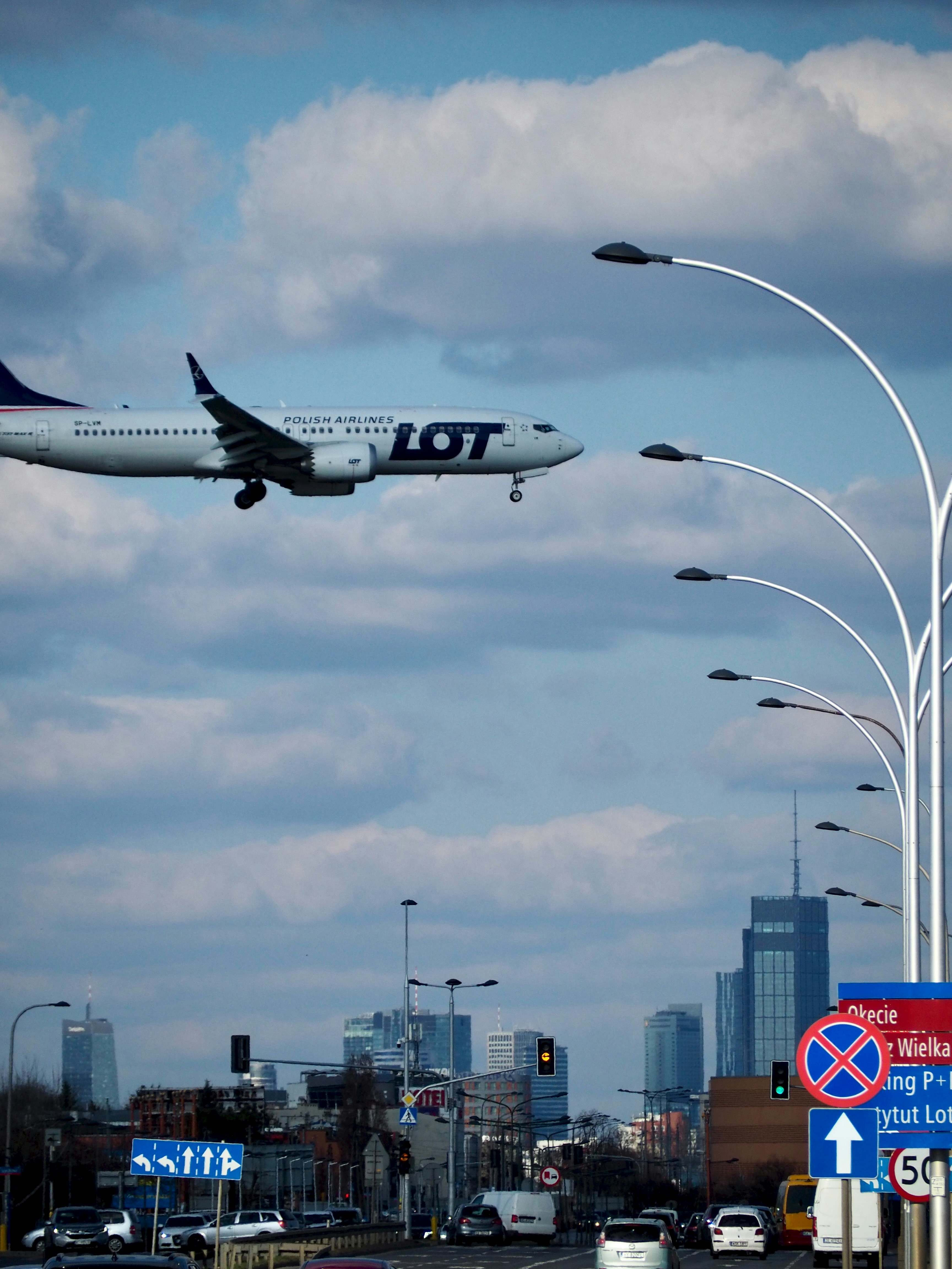 Landed in Progress: A LOT Polish Airlines jet glides above a city street under curving street lamps