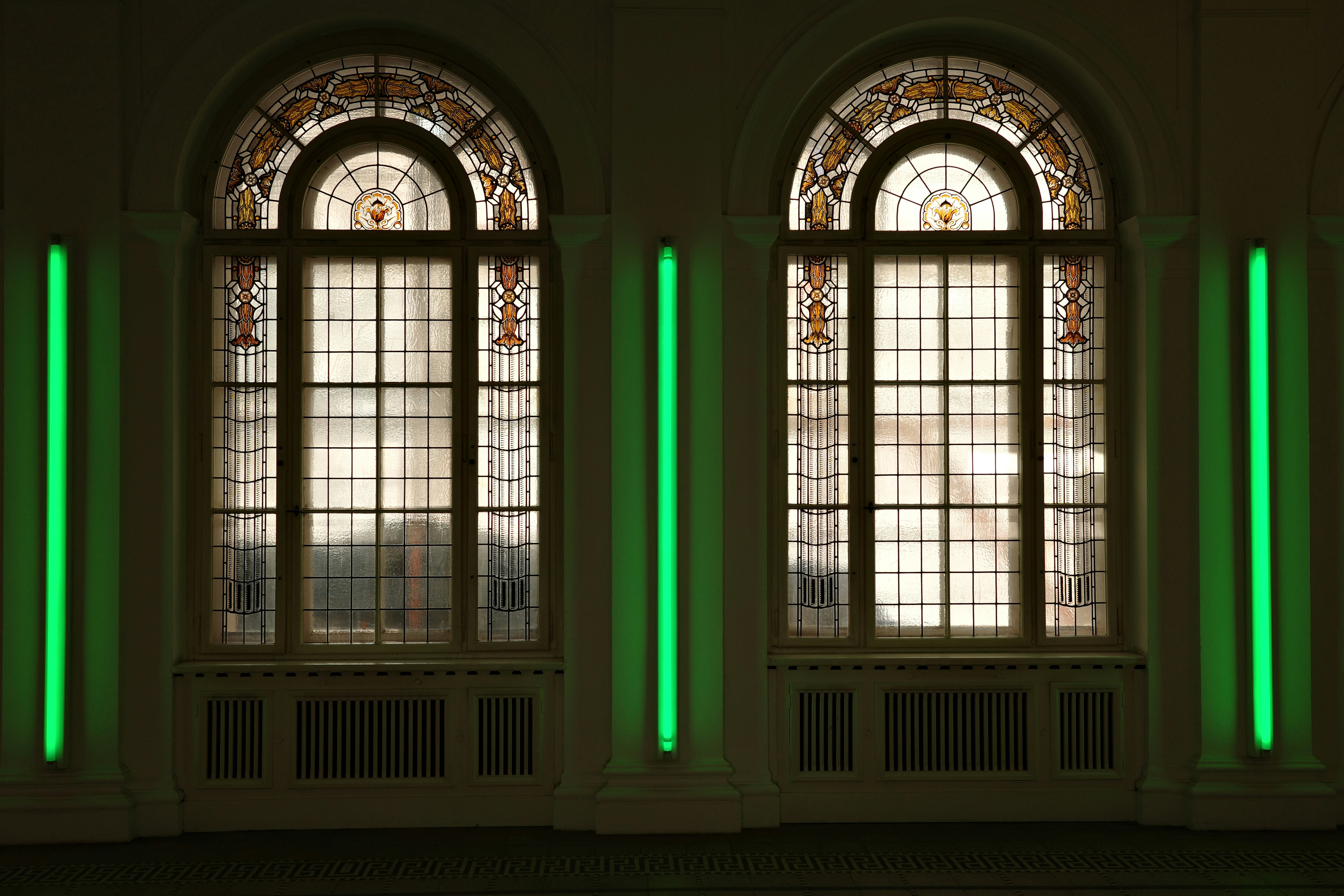 Green Neon Beams Between Arched Windows in Dim Hallway
