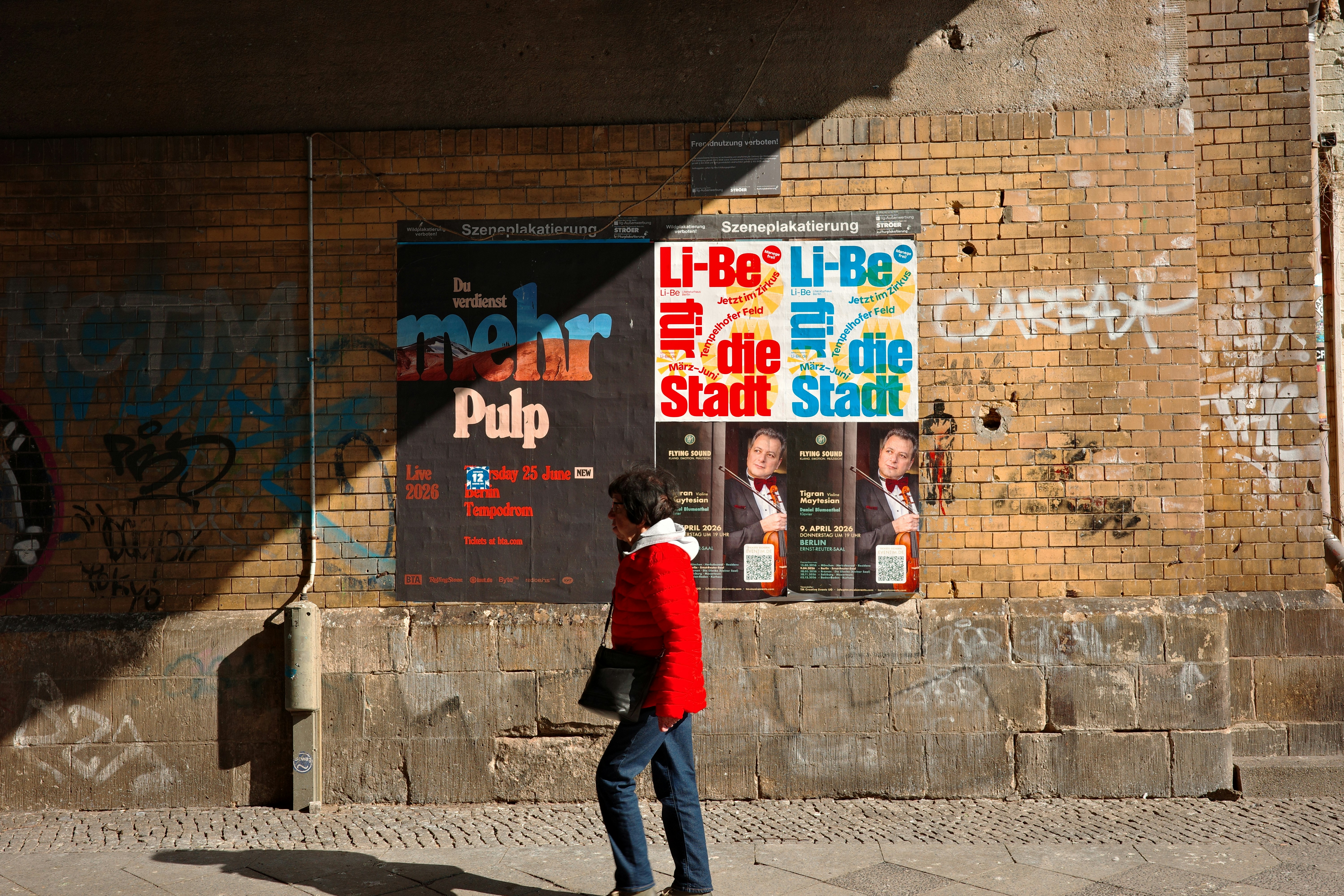 Red Coat, Quiet Walk: A Figure Passes the Wall of Posters