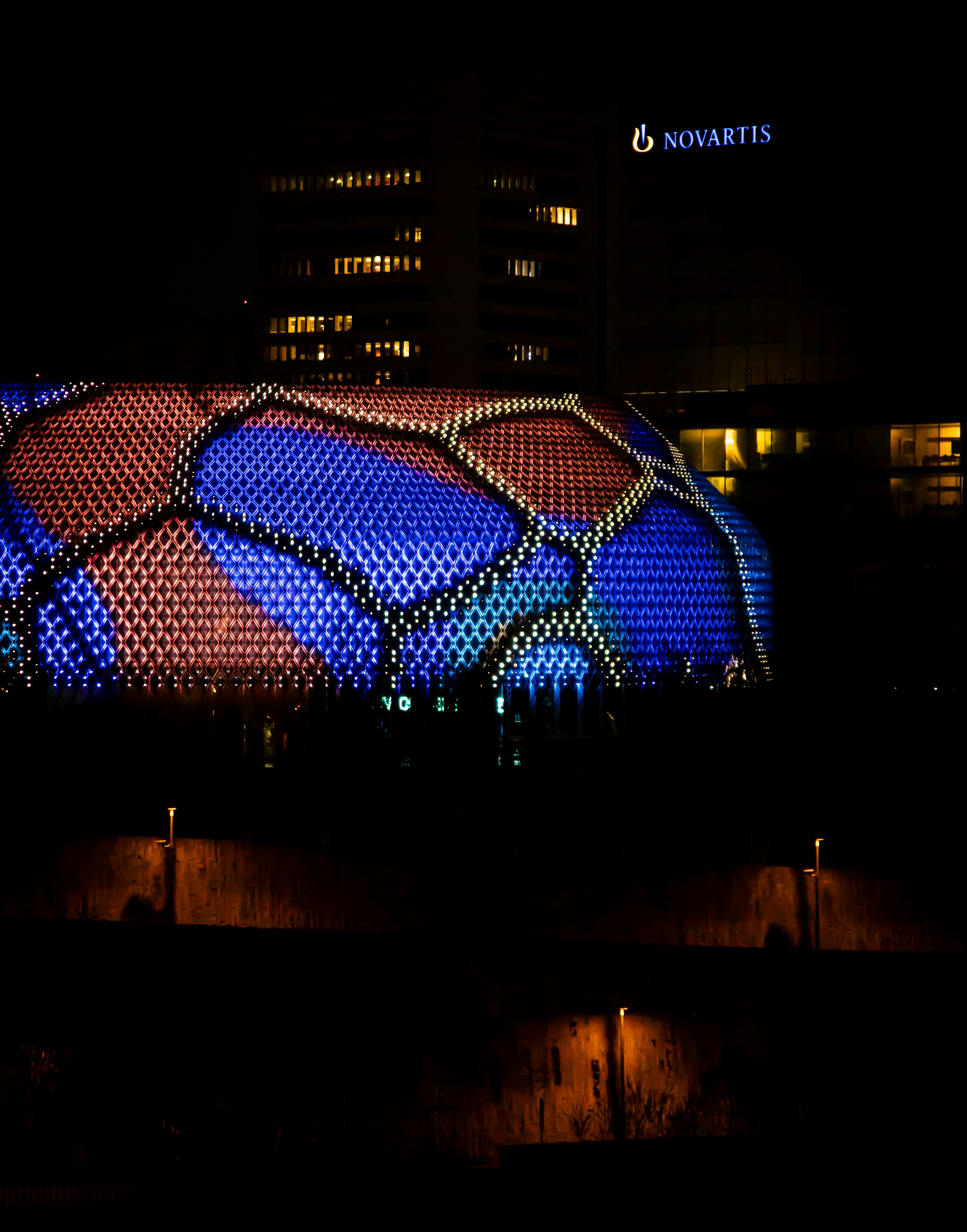 Neon Mosaic Beneath a Distant Novartis Crest