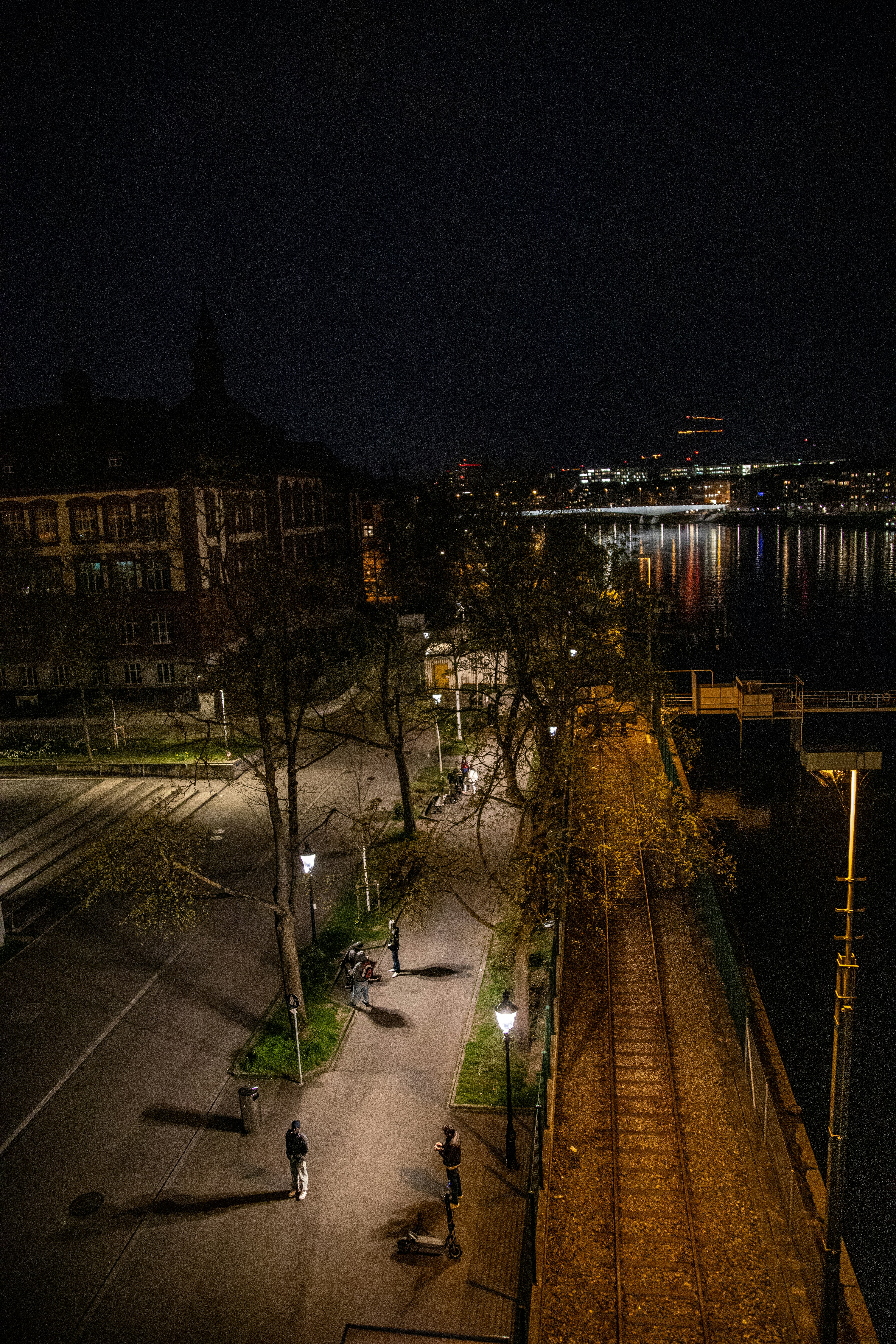 Night at the River Promenade: Streetlamps, Rail Track, and Quiet Figures