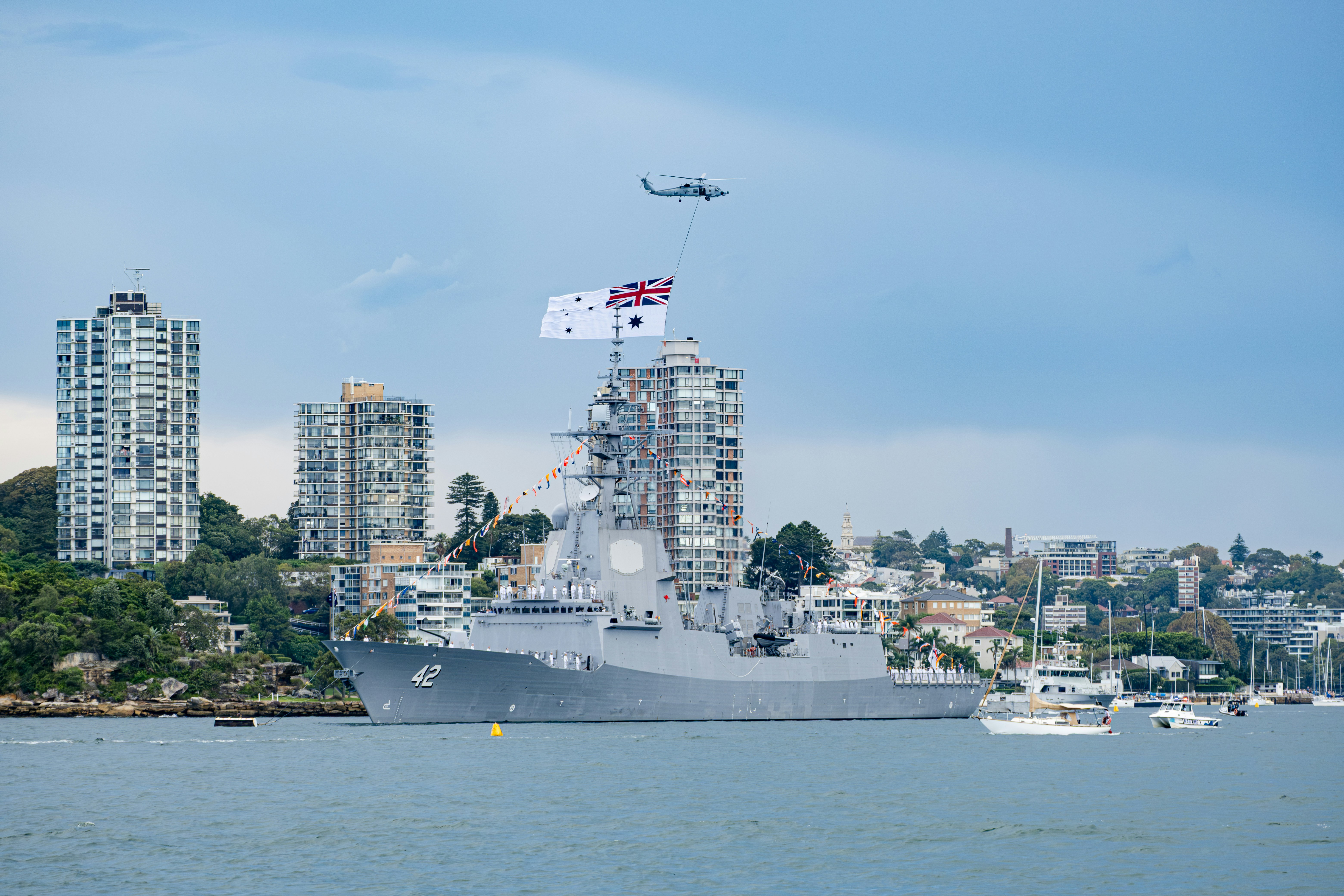 Grey Warship Steady in Port: Flags and Skyline in Calm Waters