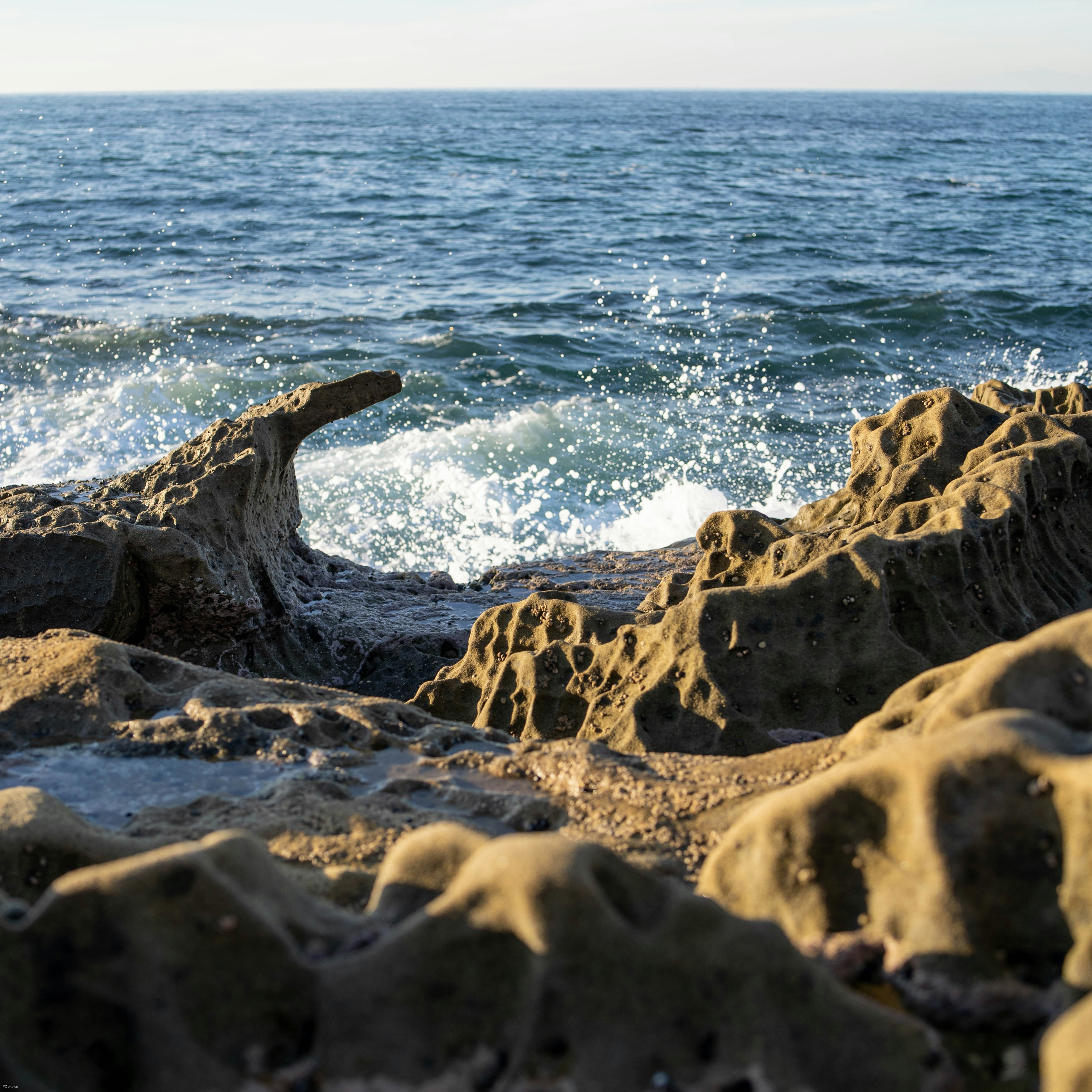 Rugged shoreline kiss: sunlit jagged rocks meeting the ocean