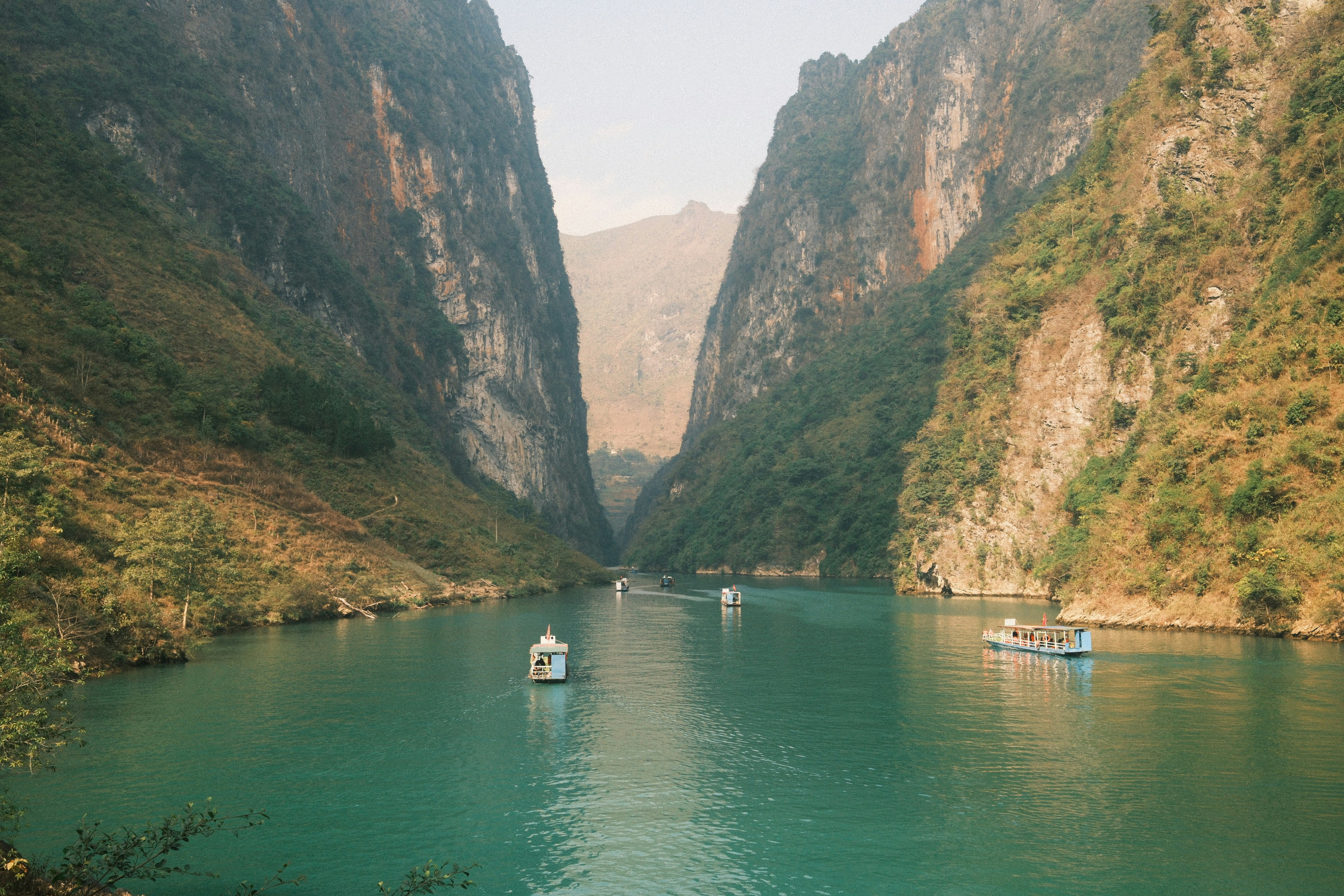 Boats drift through a emerald gorge beneath towering cliffs