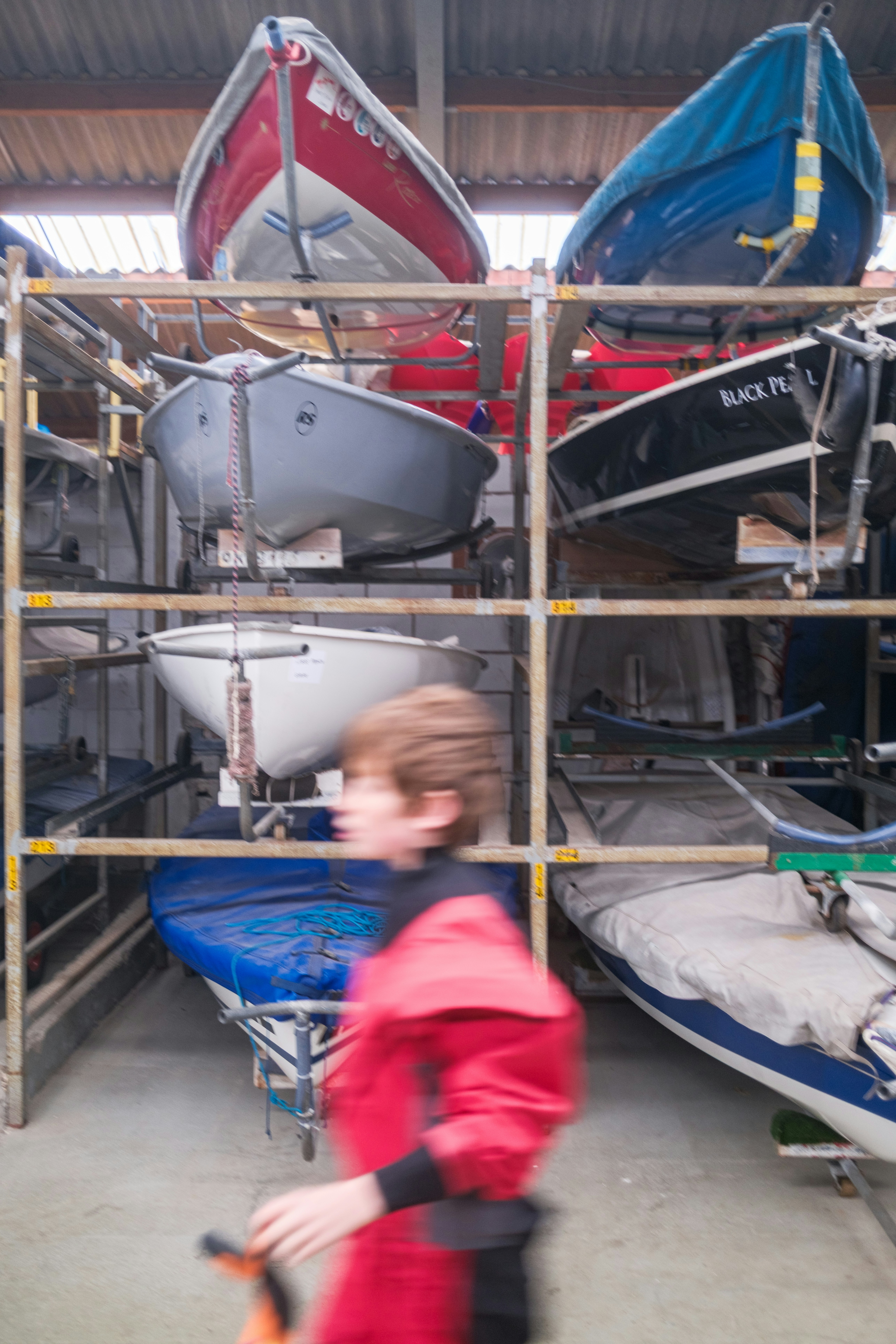Blurred Passage Through a Boat Storage: A Child in Red Amid Boats