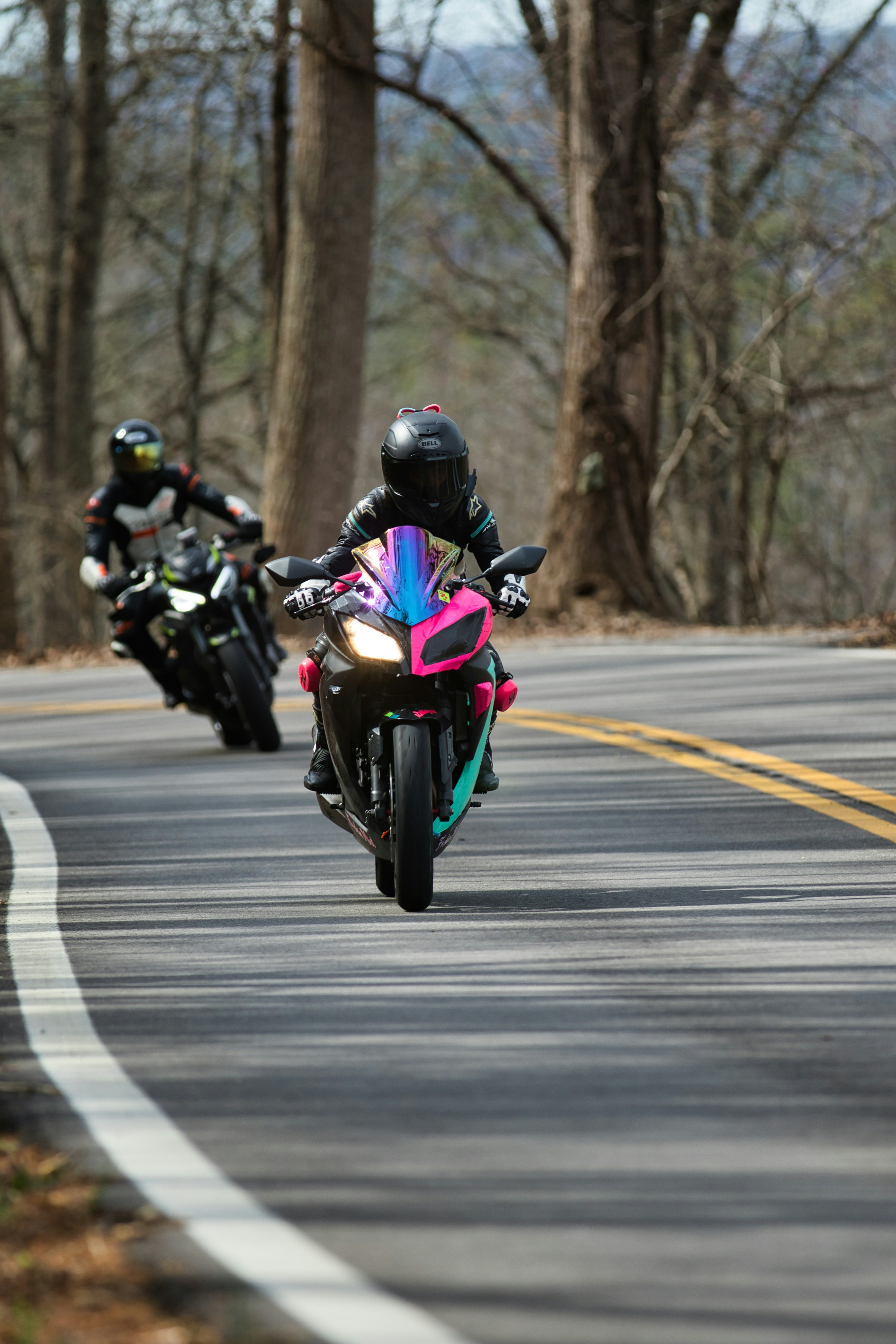 Neon-coated sprint: a bold sportbike leads a lone rider through a forested curve