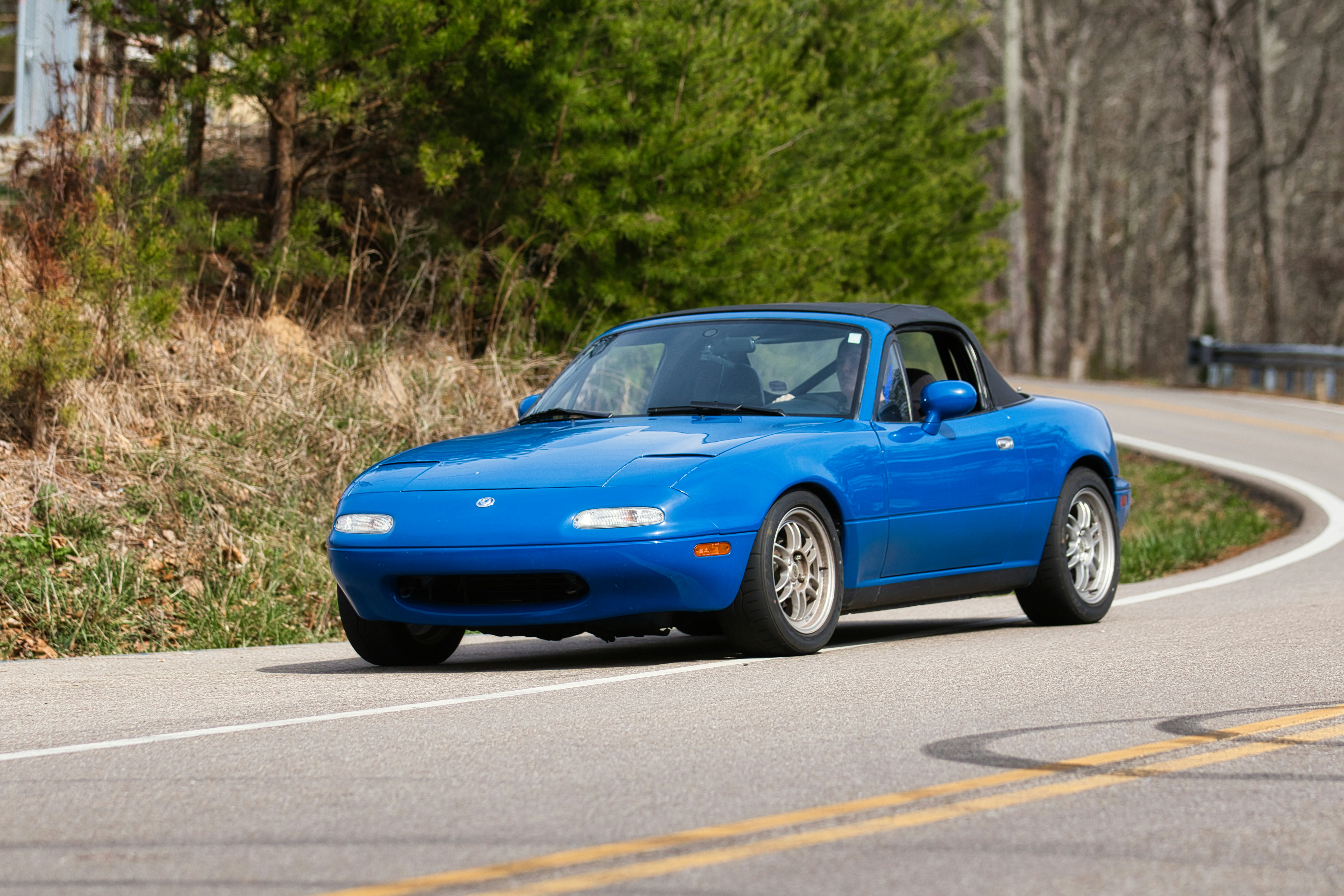 Blue sports car rounds a bend on a winding country road