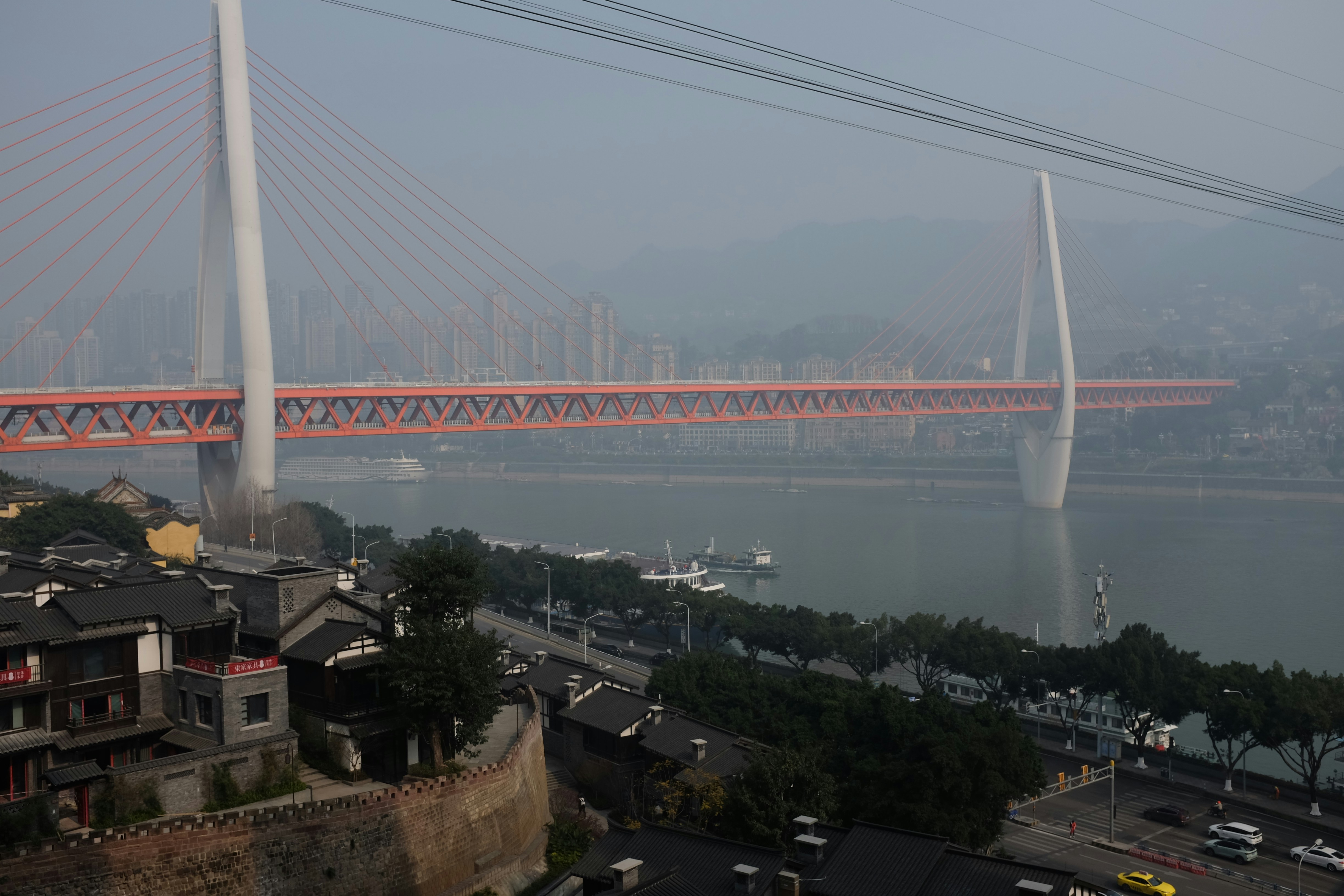 Overcast Riverside Arc: A Suspension Bridge Framed by a Historic Port City
