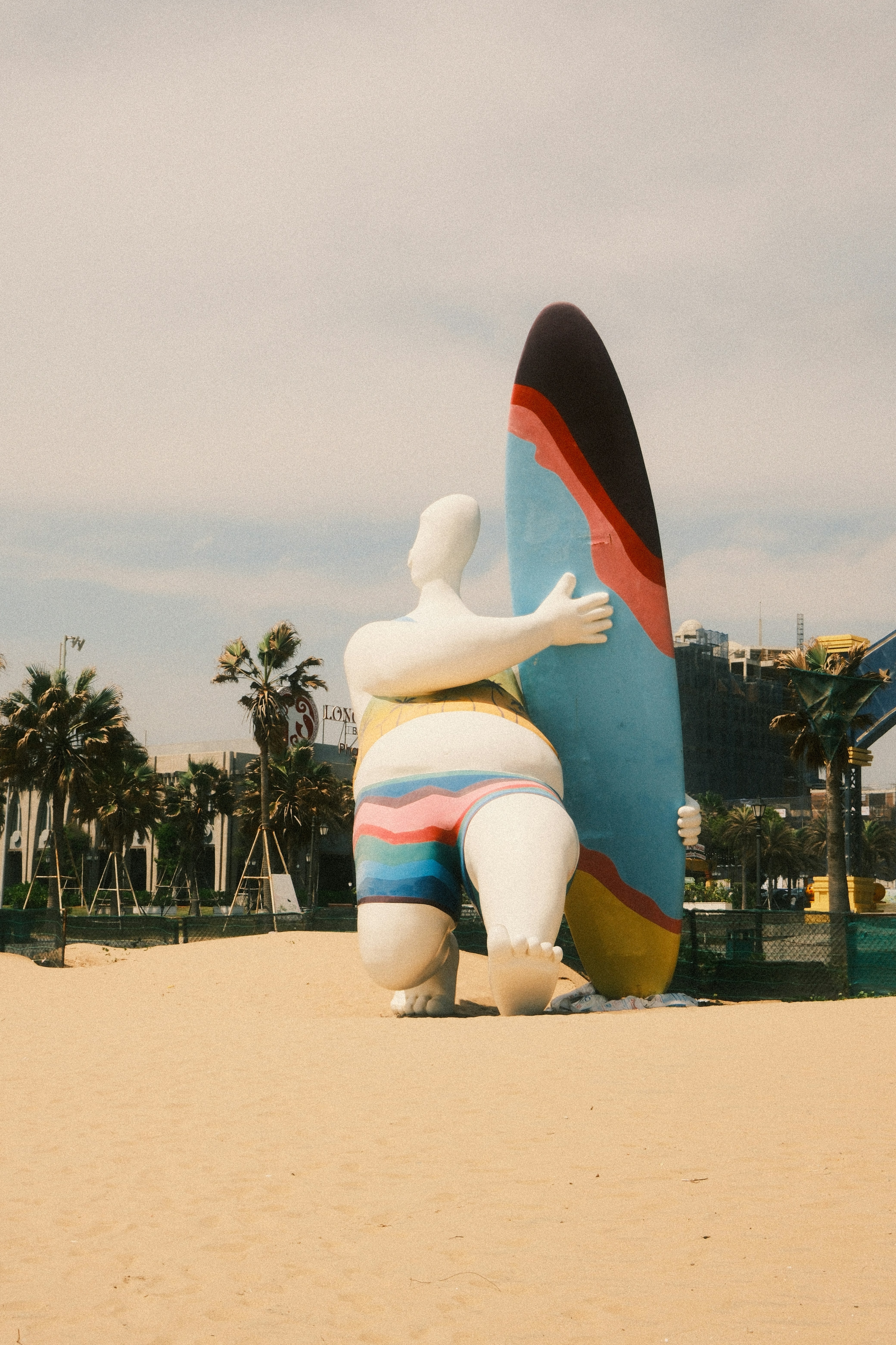 Surfing Figment: A Giant Statue Embracing a Colorful Board on Sunny Sand