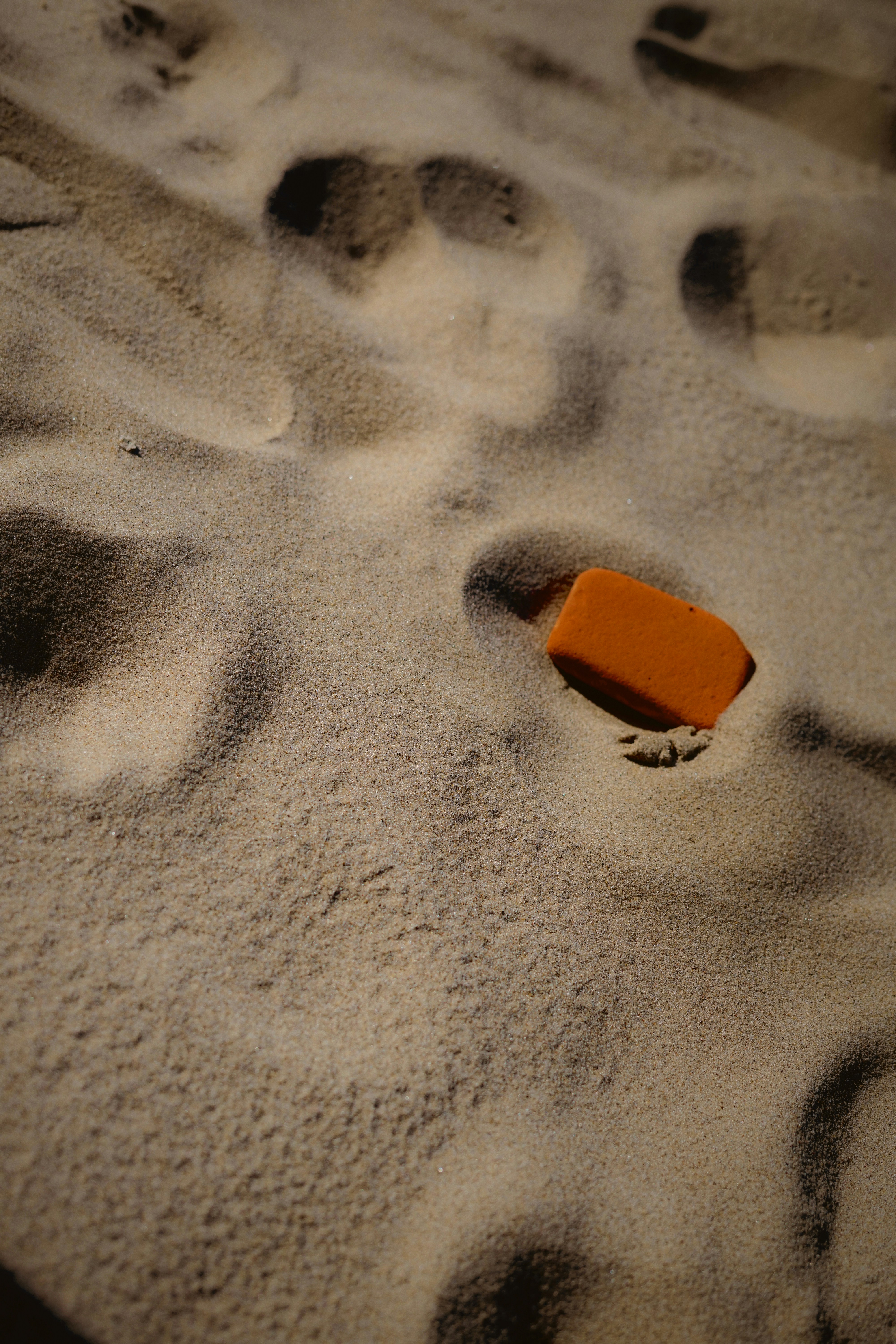 A lone orange brick rests in a windswept desert of pale sand