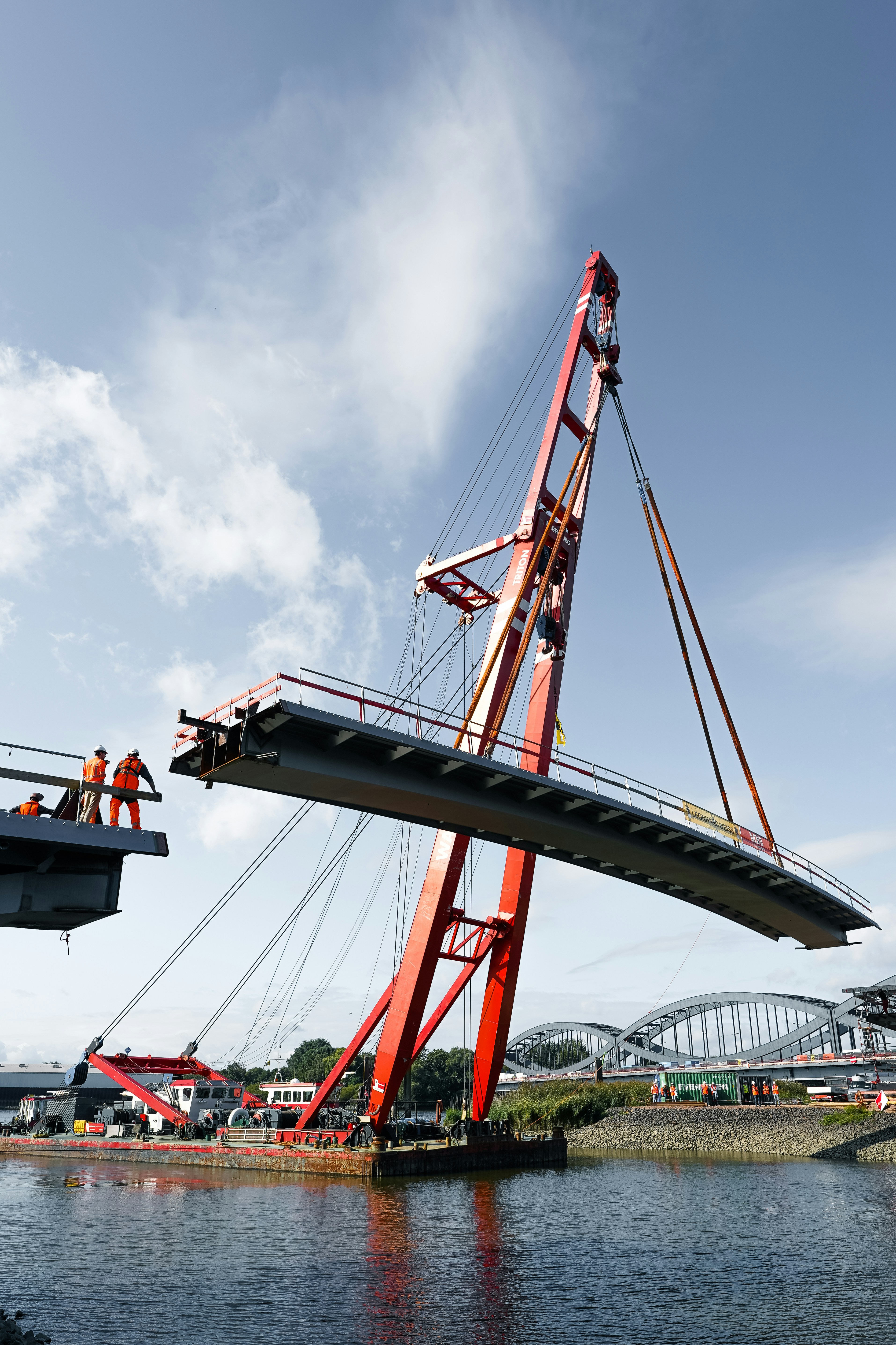 Lifting Span: A Red Maritime Crane Elevates a Partially Assembled Bridge
