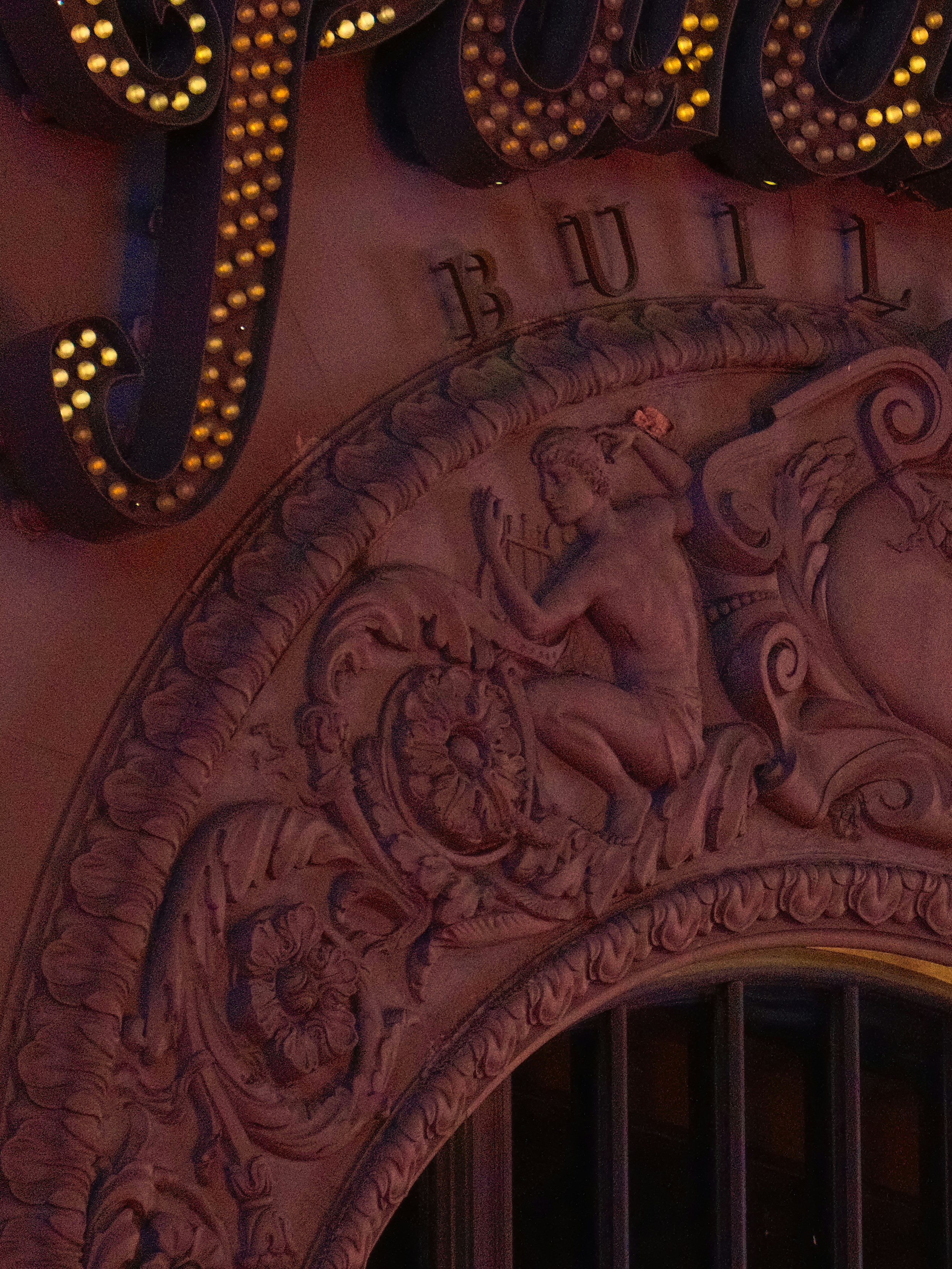 Backlit Mural Arch: Carved Cherub Amid Neon Letters