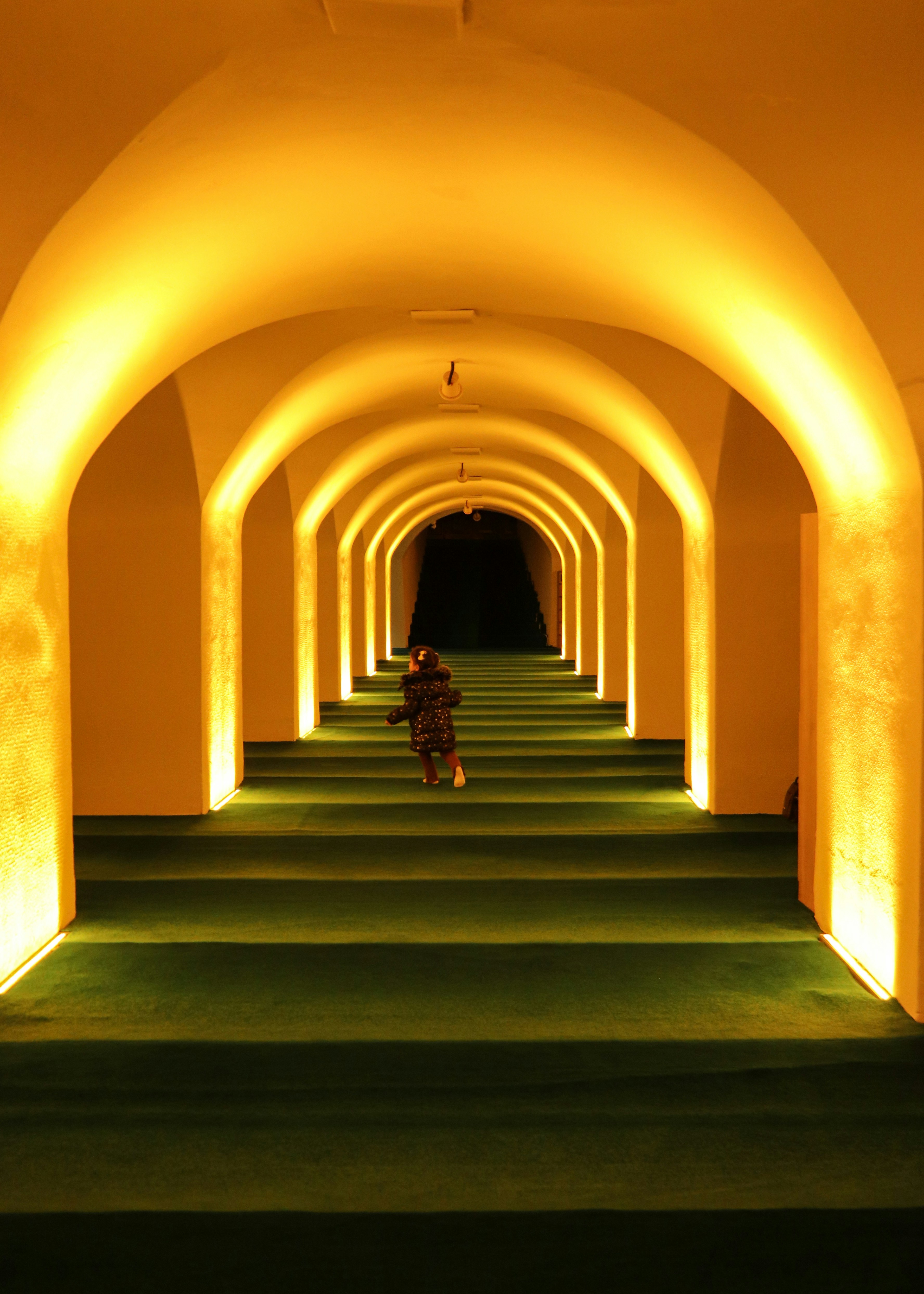 Golden Archways: A Child’s Quiet Pause in a Radiant Corridor