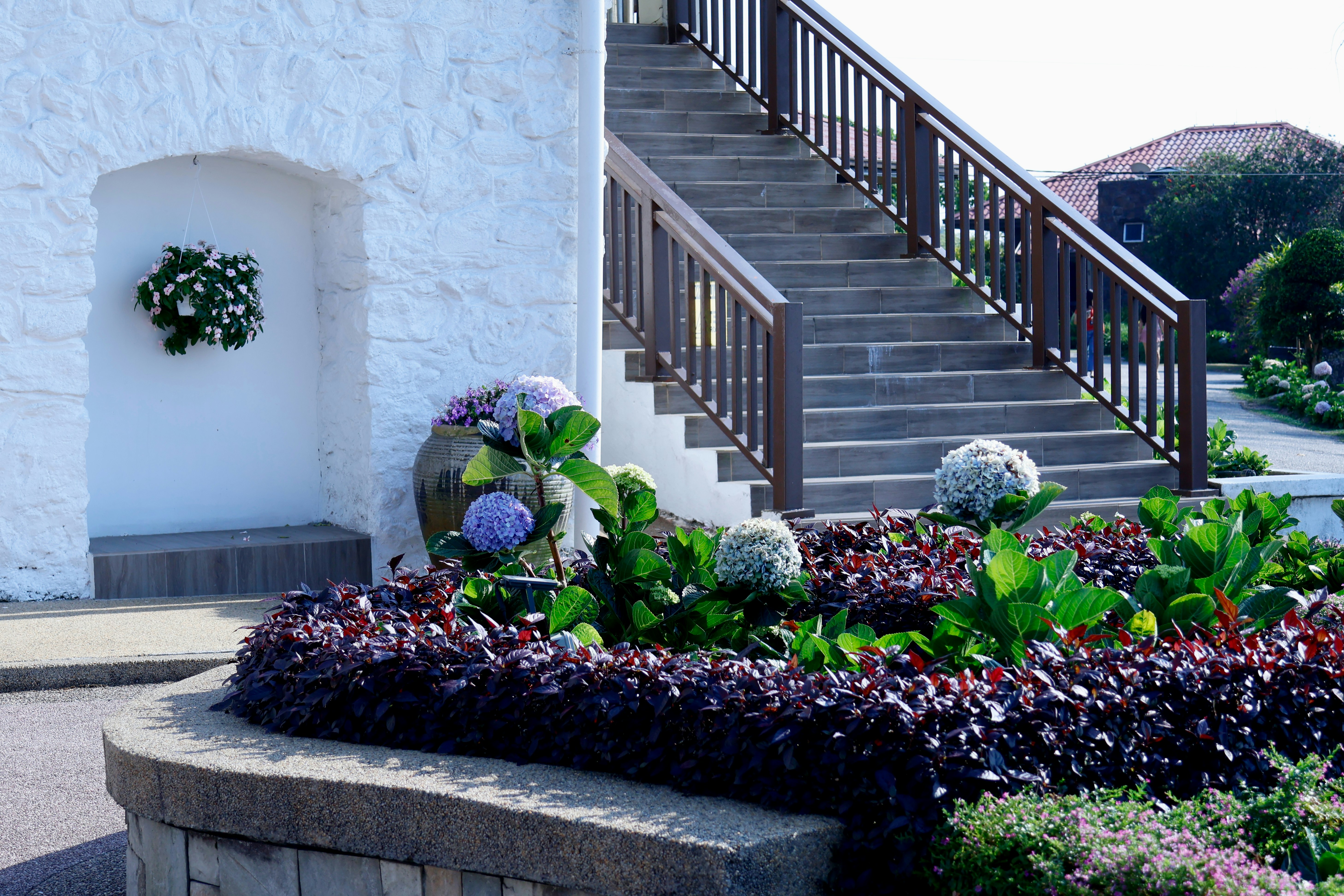Stately stairs rise beside a curated flower bed under a white-washed arch