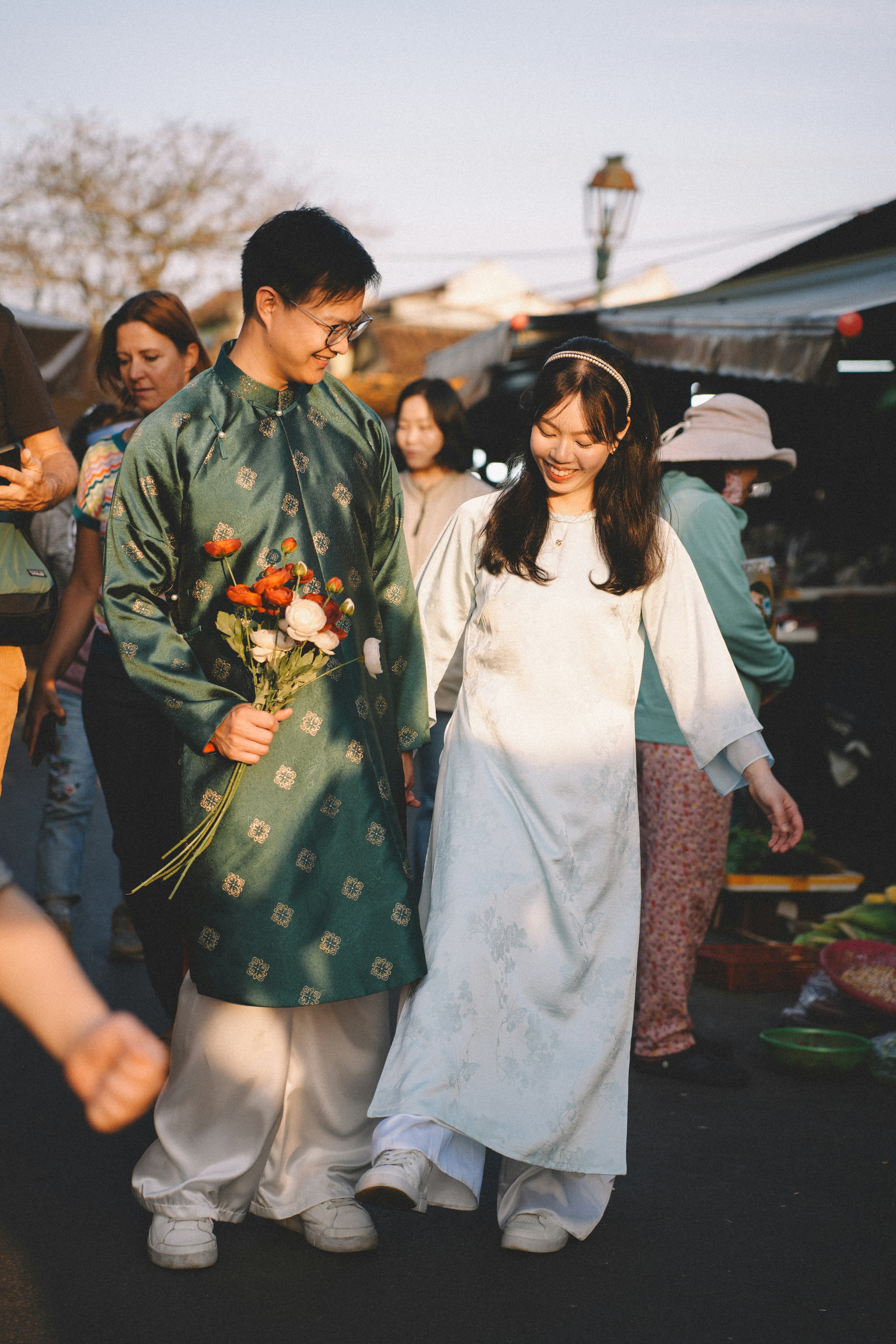 Bride and Groom in Traditional Attire Share a Joyful Moment at a Market Parade