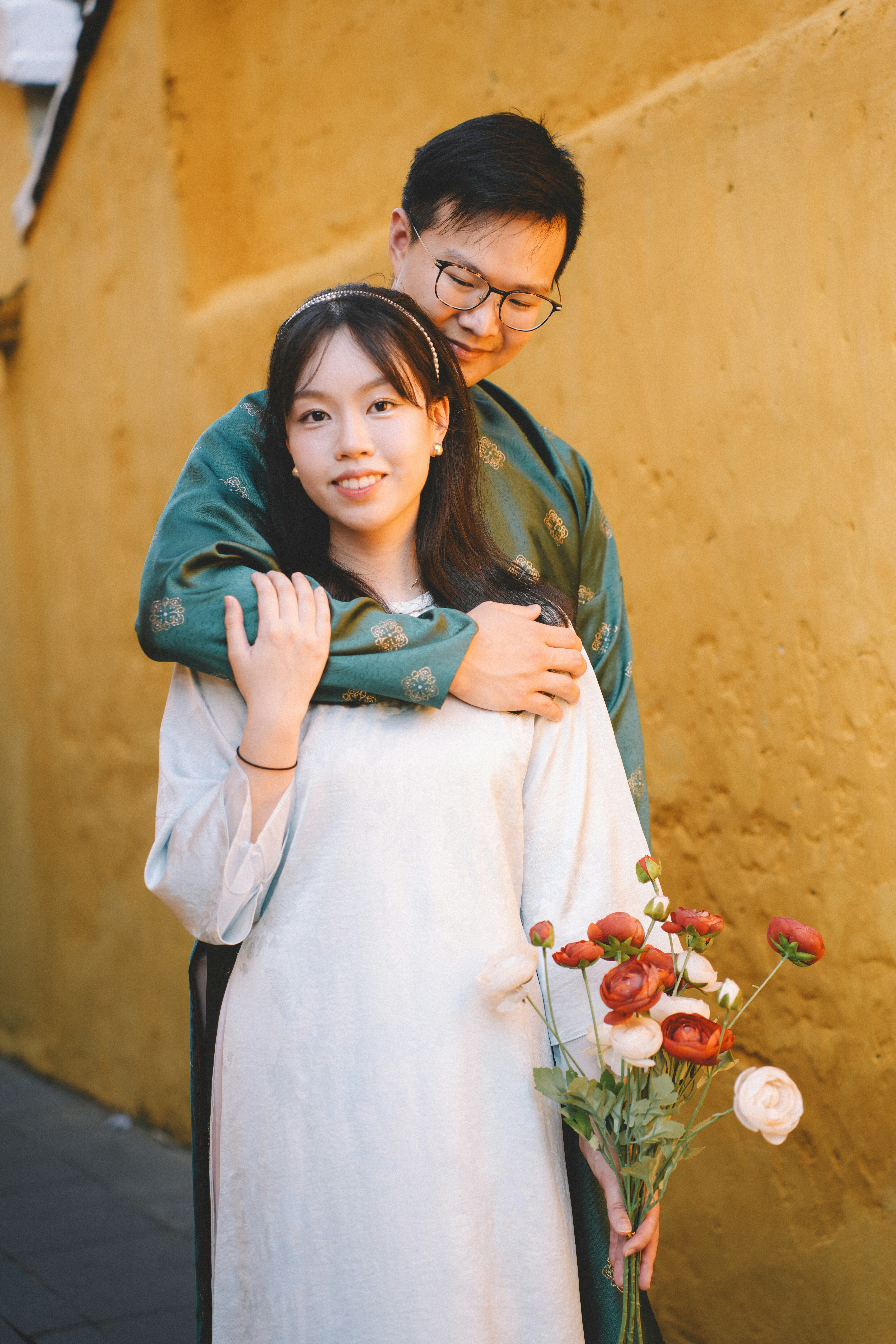 Couple in a sunlit courtyard: warmth, embrace, and bouquet of blooms