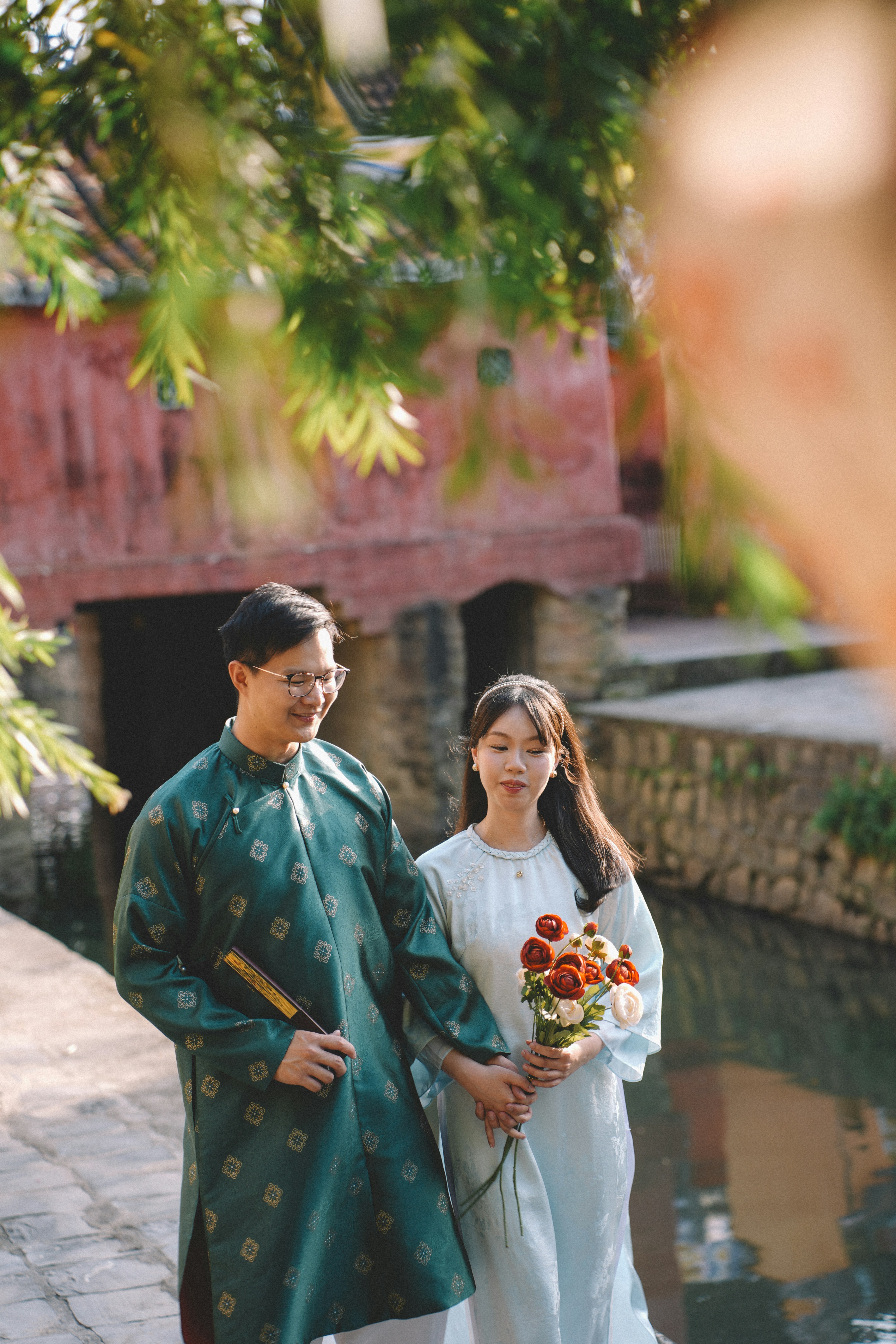 Couple in traditional attire by the canal, holding flowers