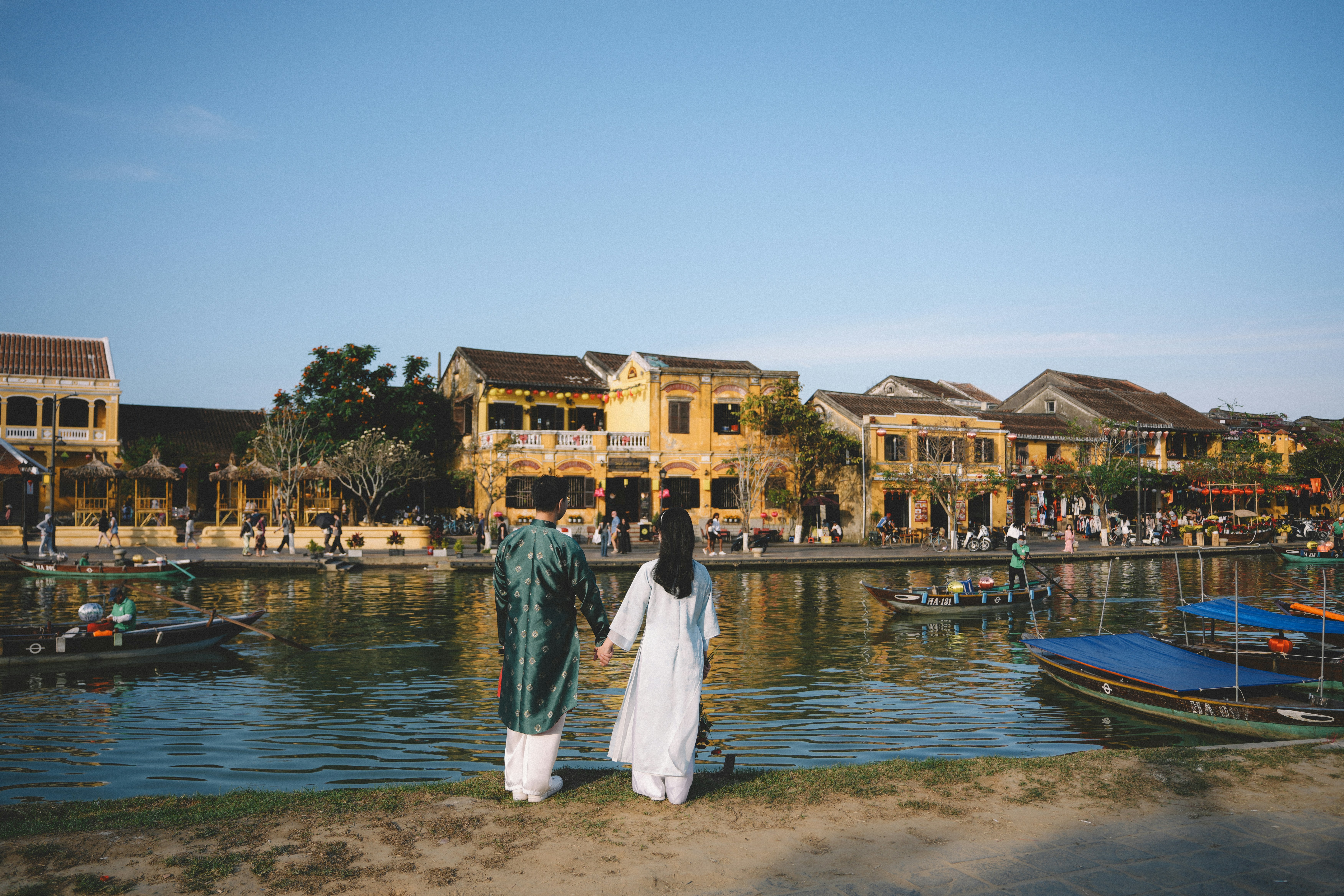 Waterfront Stroll: A Pair in White Overlook a Vibrant Hue of Riverside Town