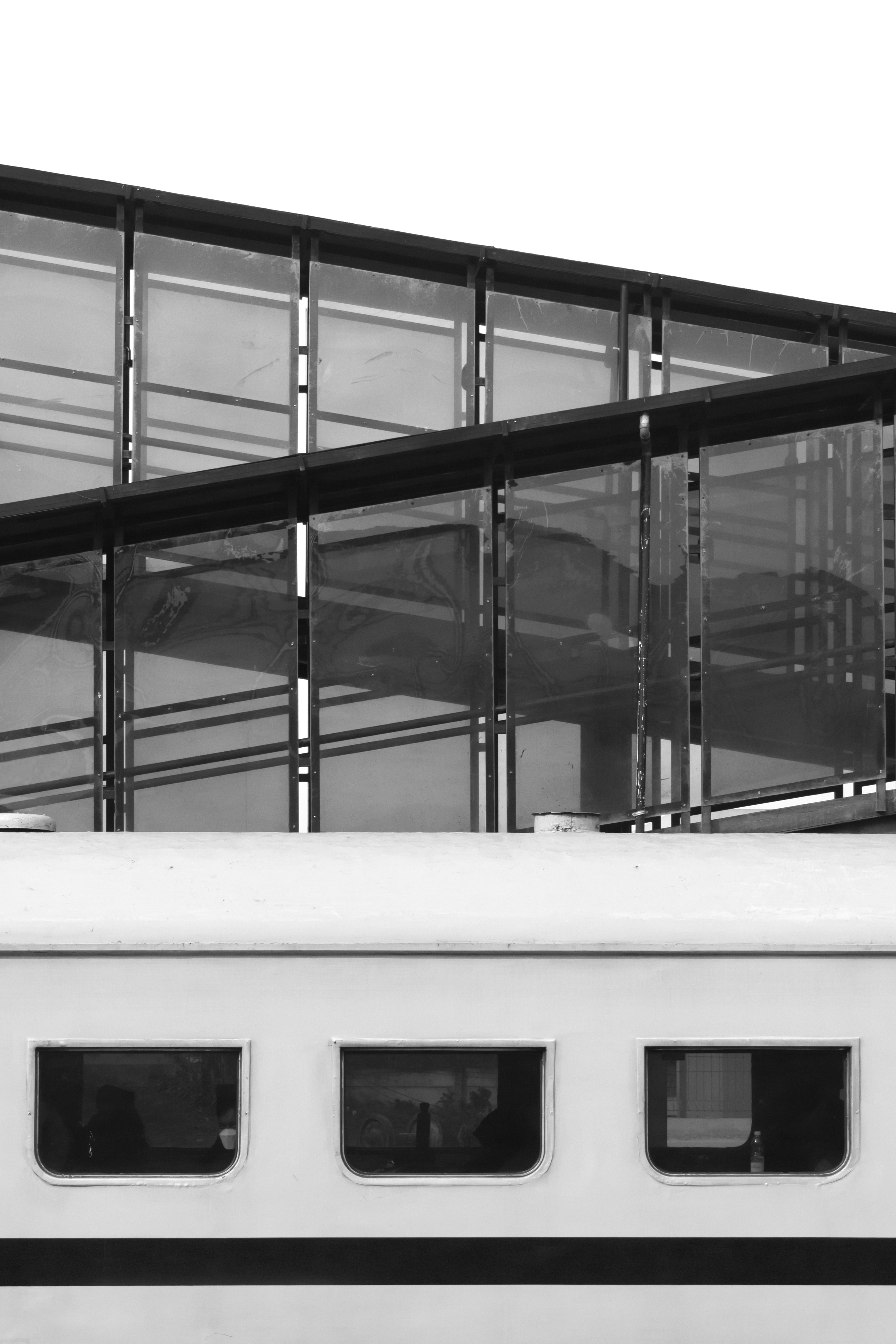 Monochrome composition showing a modern glass facade with vertical frames resting above a white wall and row of square windows.