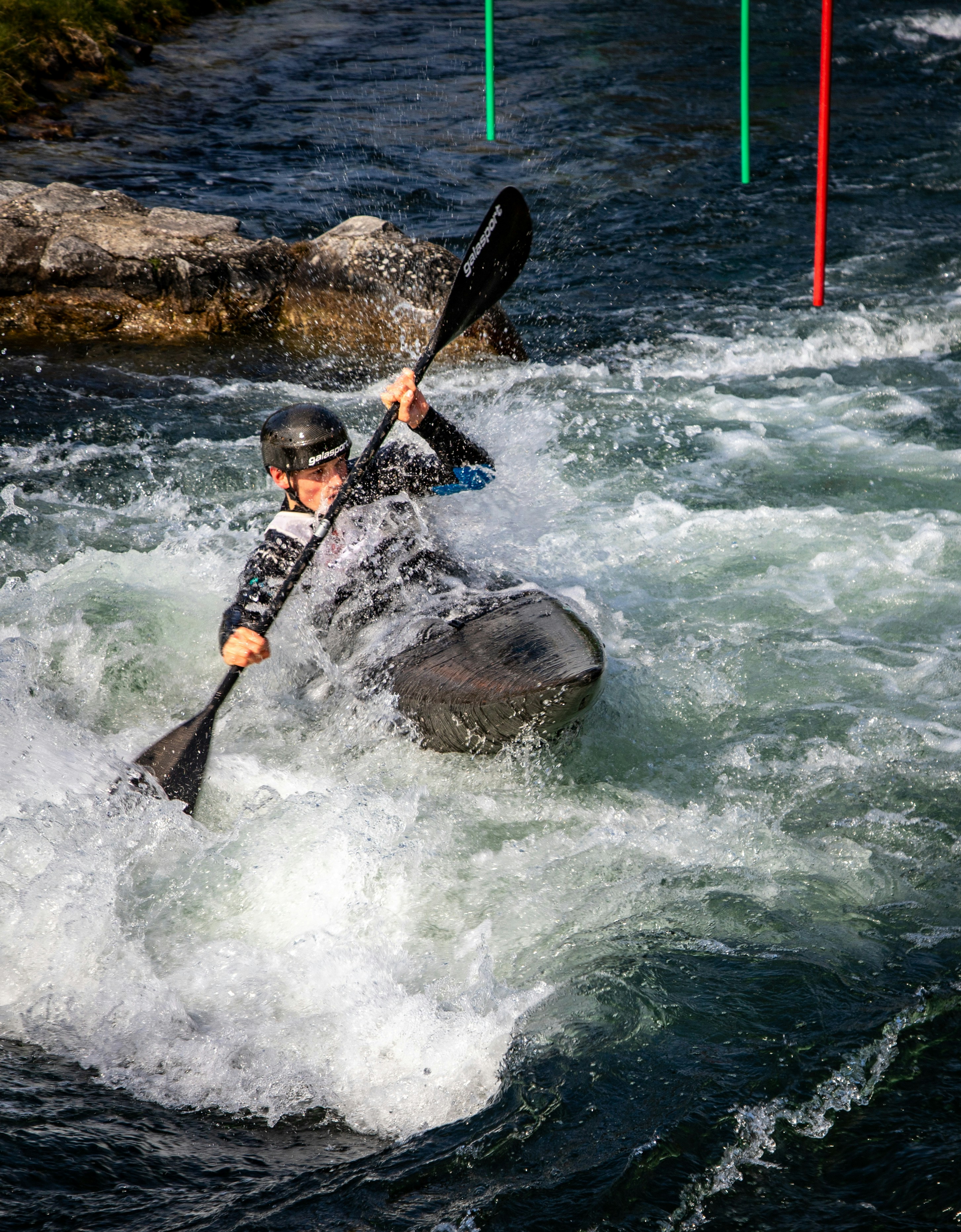 Kayaker carving through whitewater under a rocky ledge