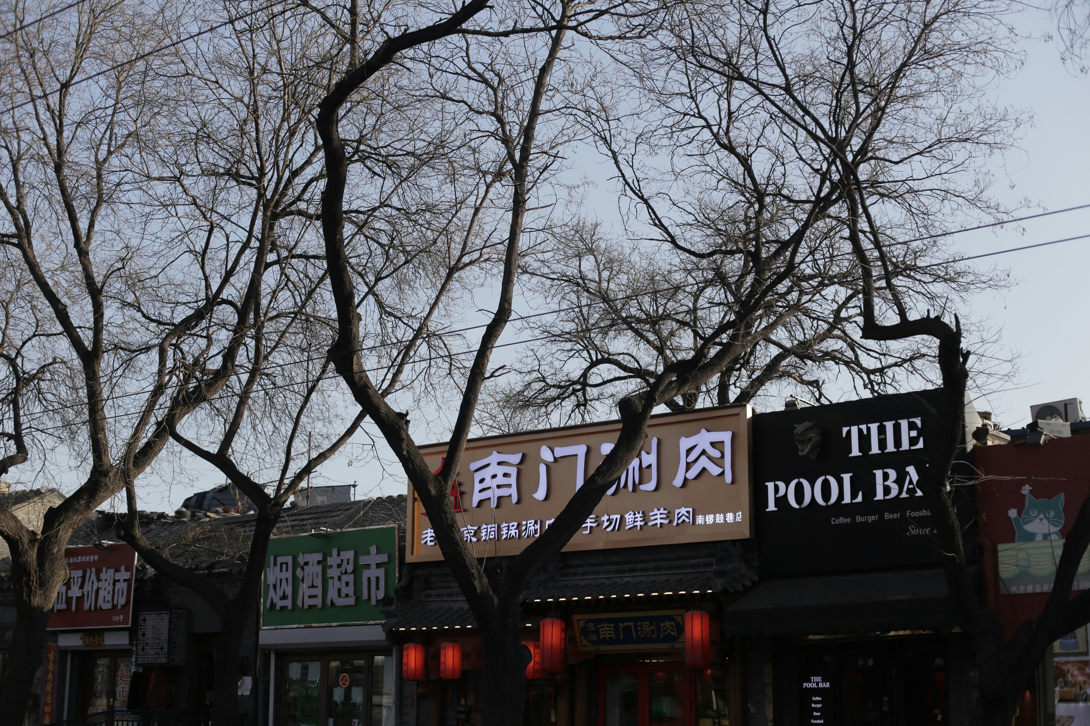 Streetfront Lanterns: Hidden Dining Signage Beneath Bare Branches