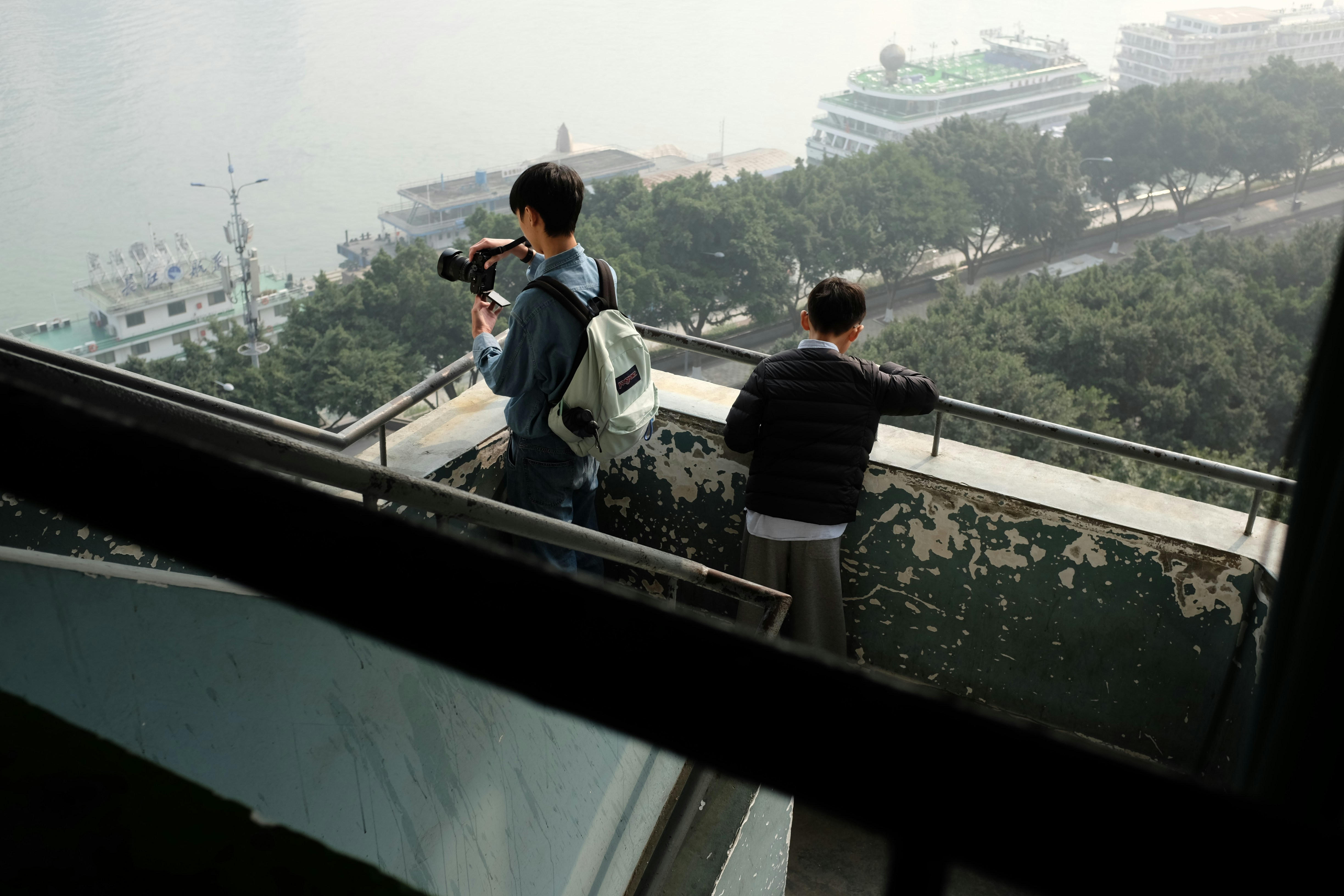 Two Onlookers on a Weathered Balcony Overlooking a Riverfront