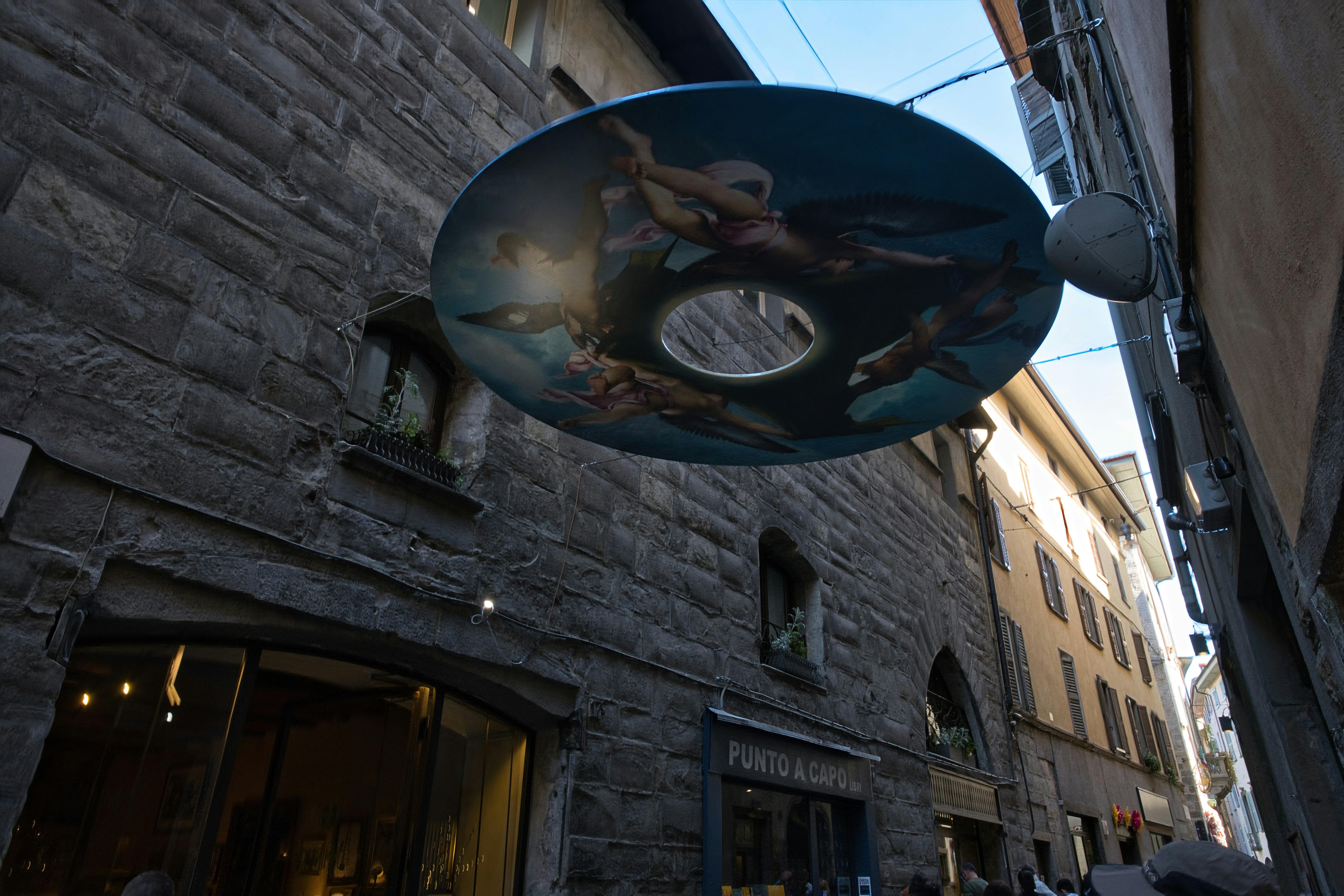 Circular mural over a narrow street cast in late afternoon light
