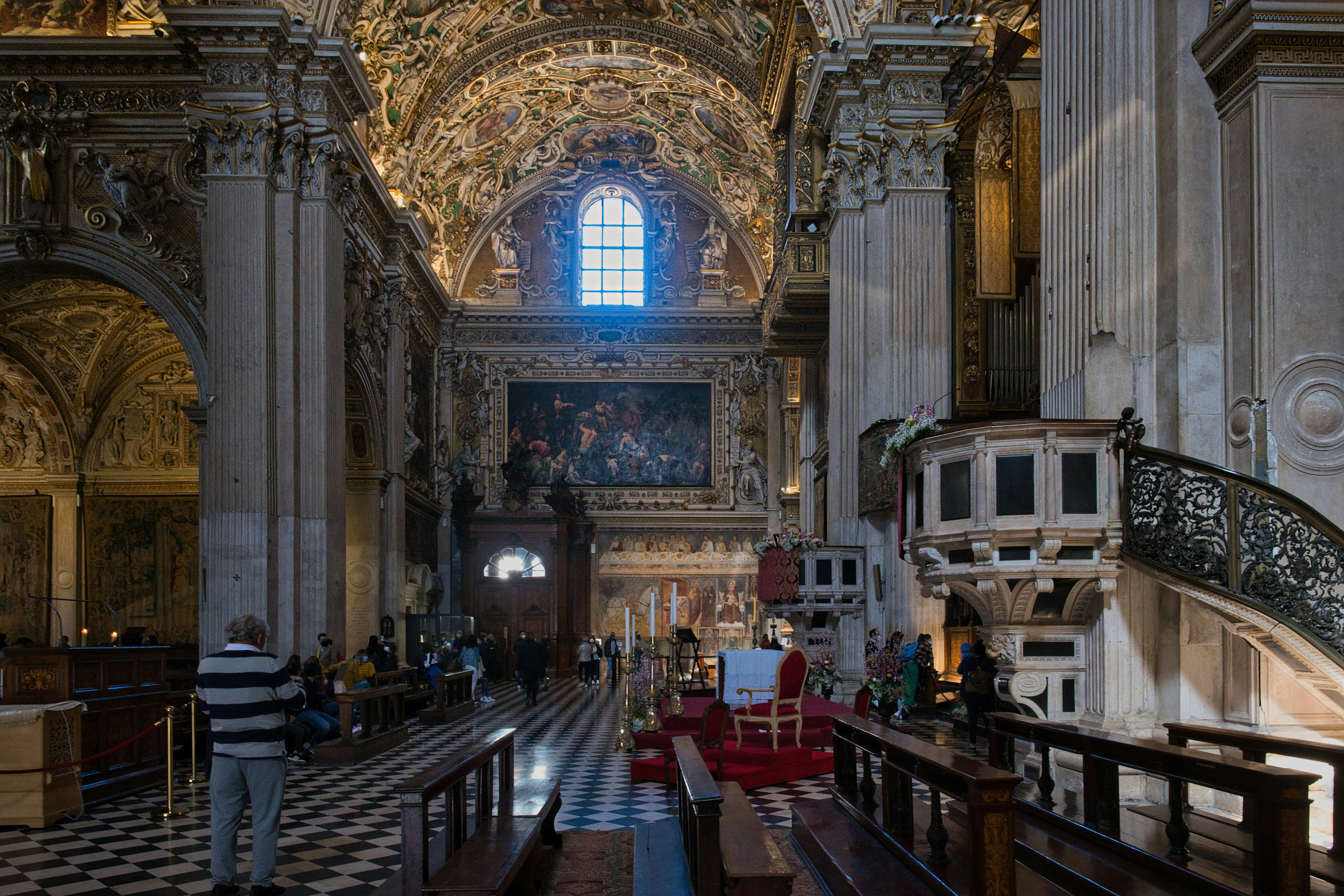 Interior of a Baroque church: ornate vaults, sweeping staircase, and pew-lined nave