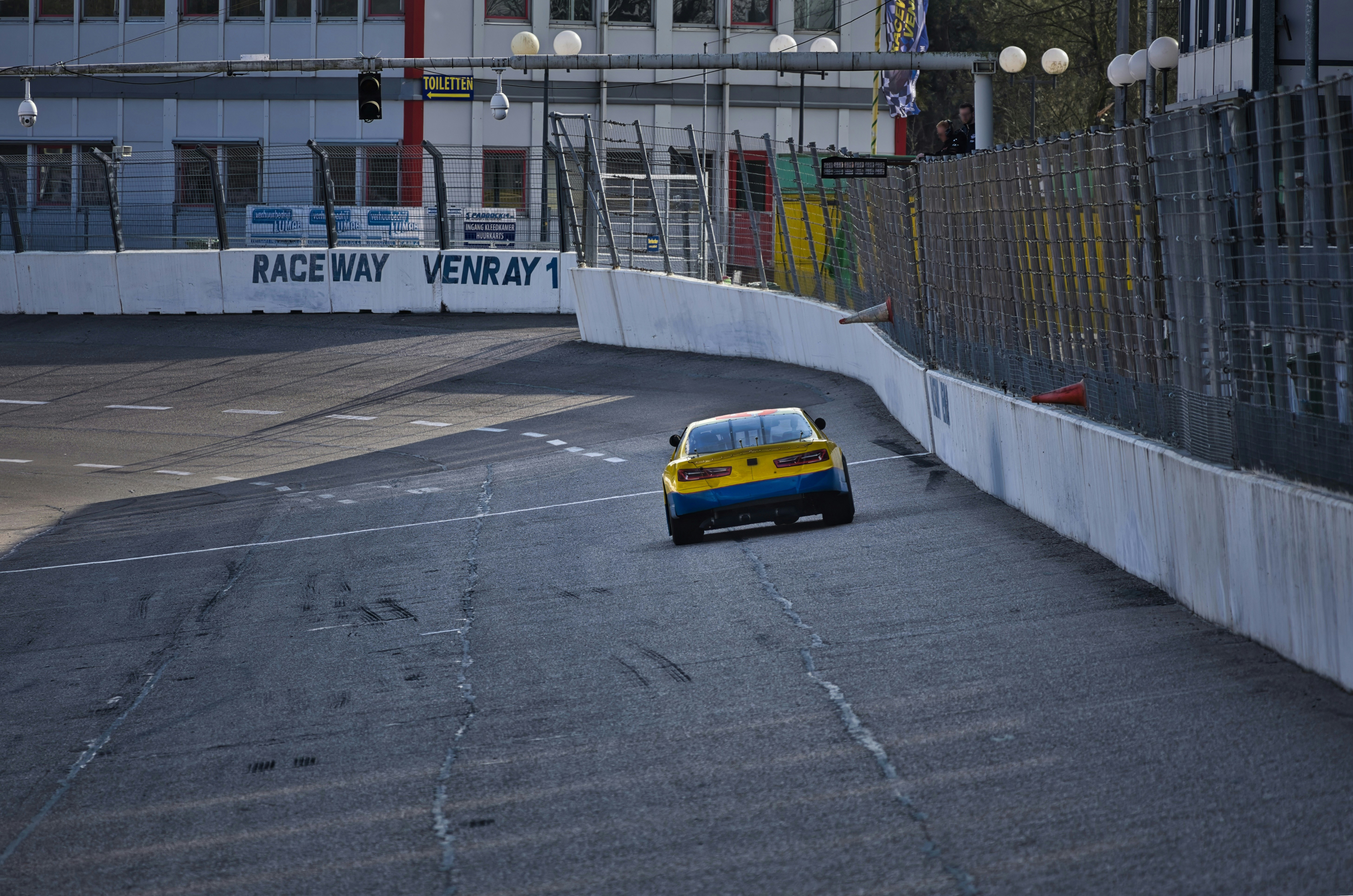 Yellow race car carving a solo line on a sunlit speedway