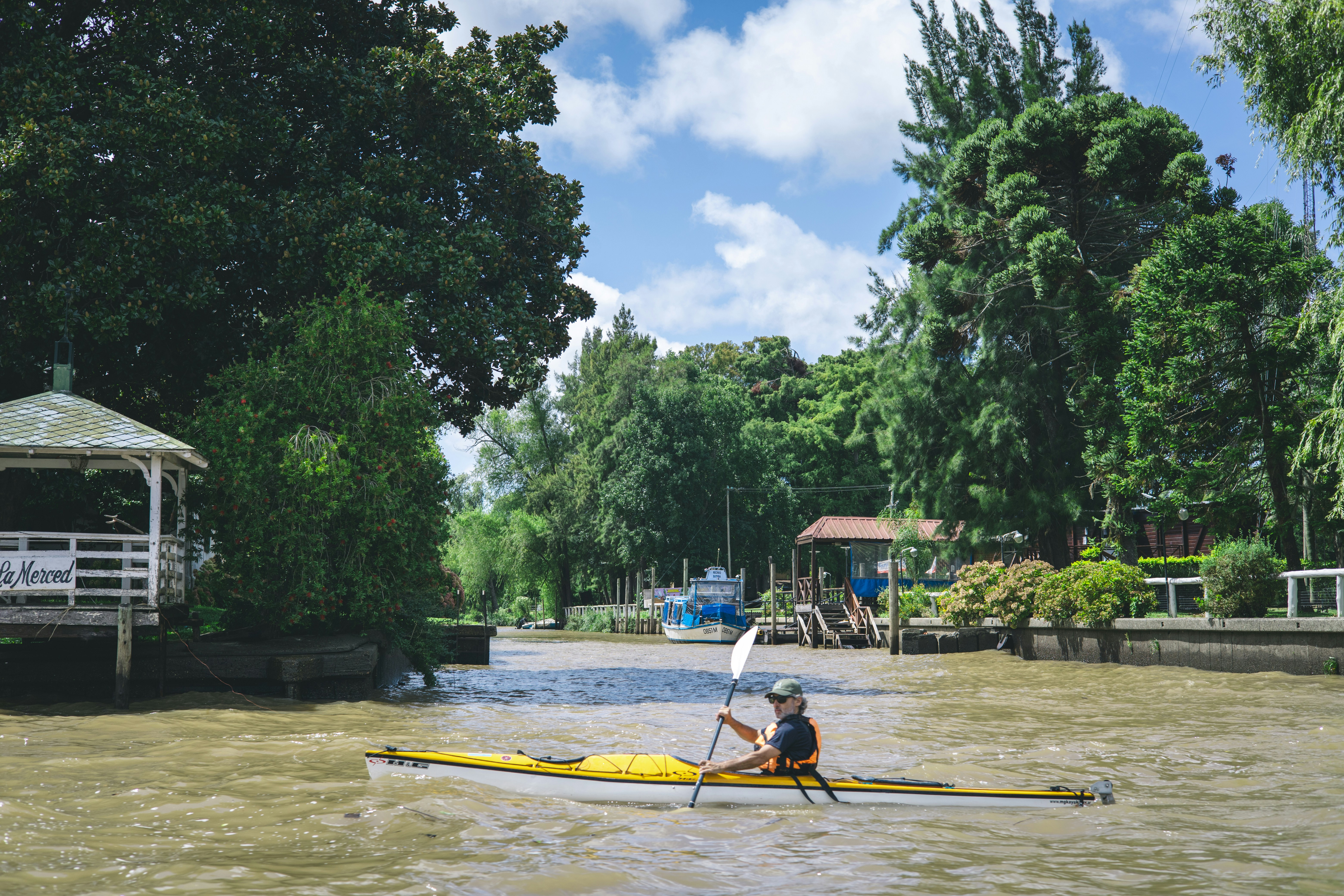 Paddler in a Narrow Boat Navigates Gentle River Through Riverside Retreat