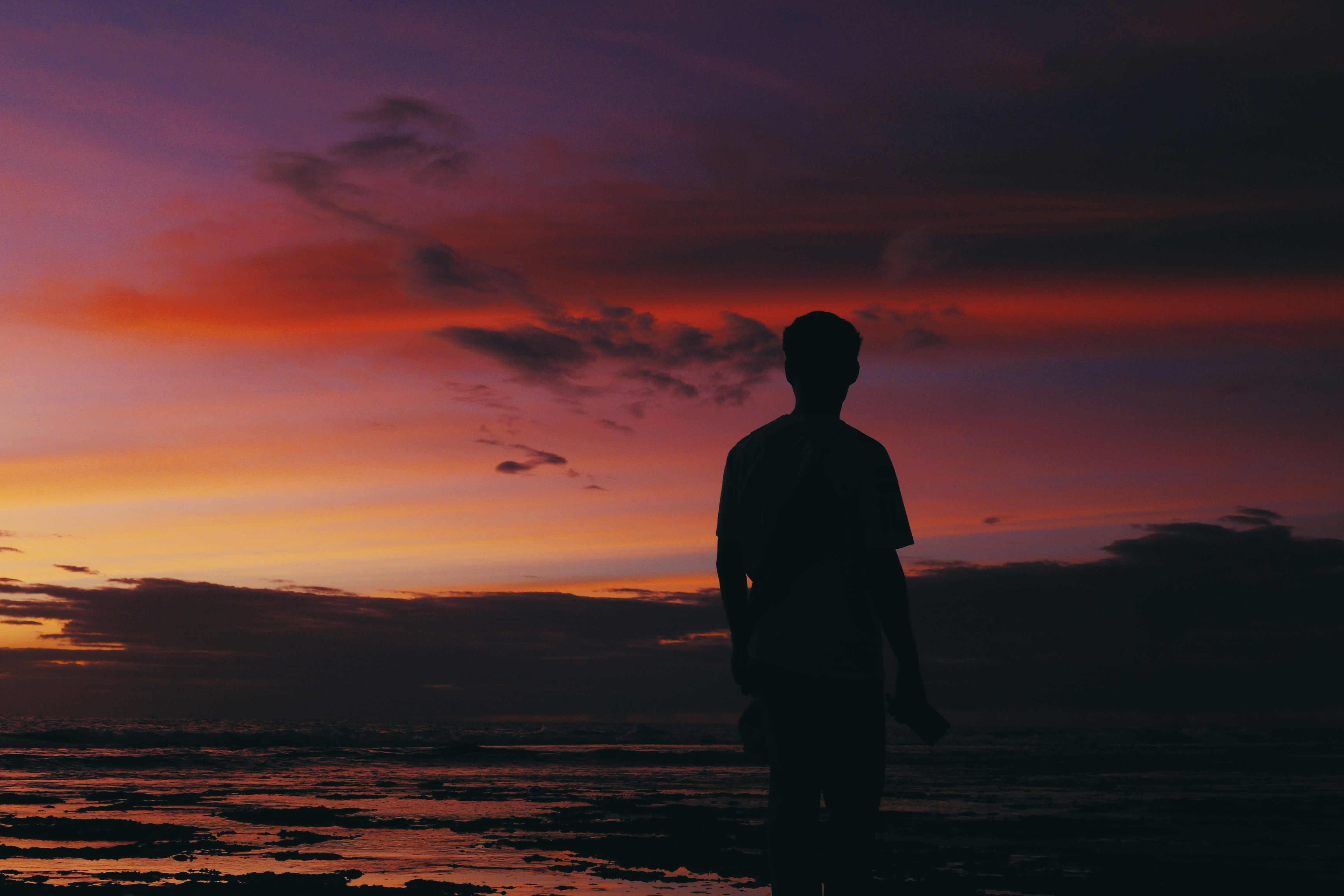 Silhouette at Dusk: A lone figure on the shoreline as the sky ignites in gradients of orange and violet