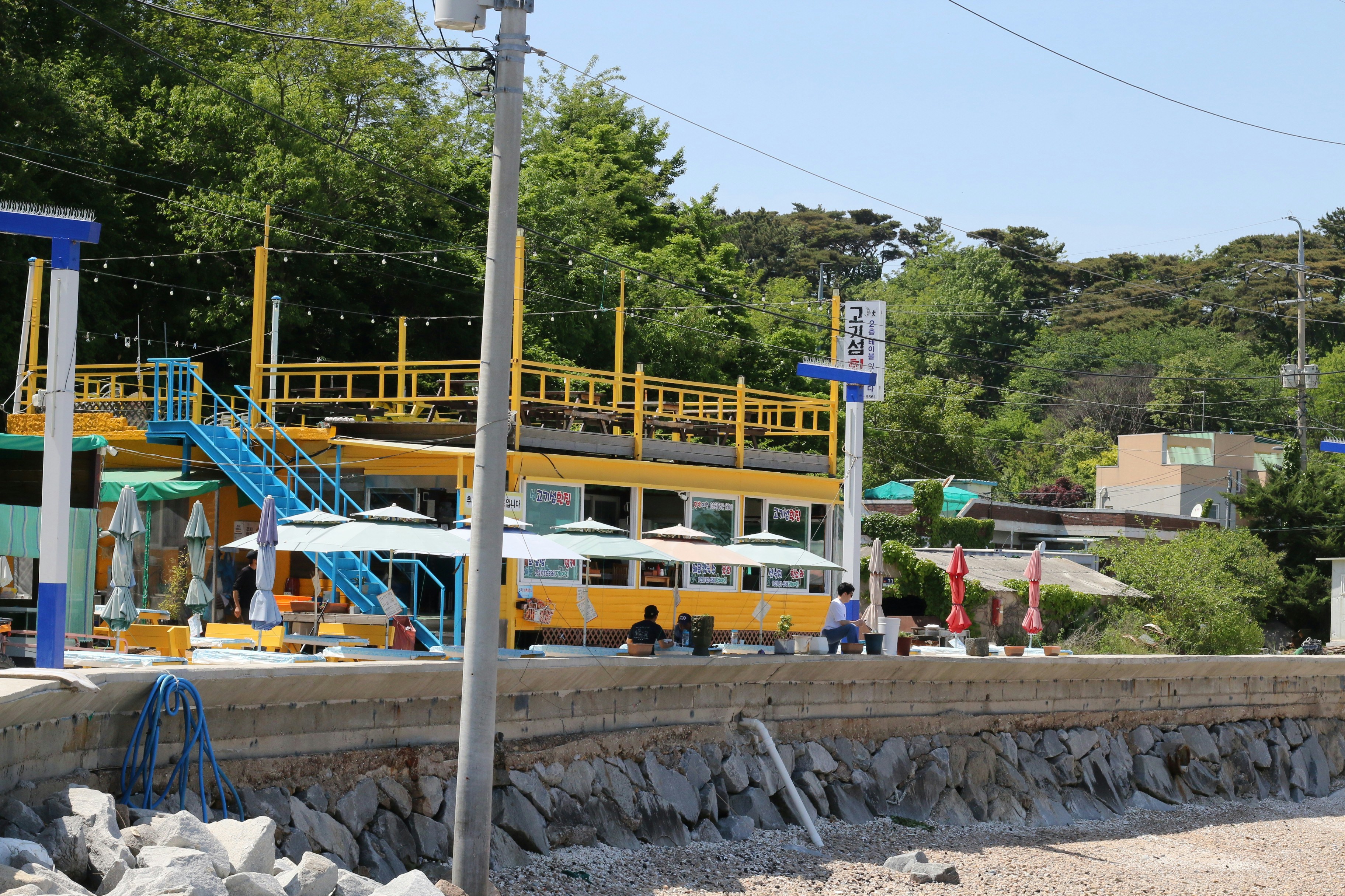 Lively seaside terrace with bright yellow and blue structures under a sunlit canopy