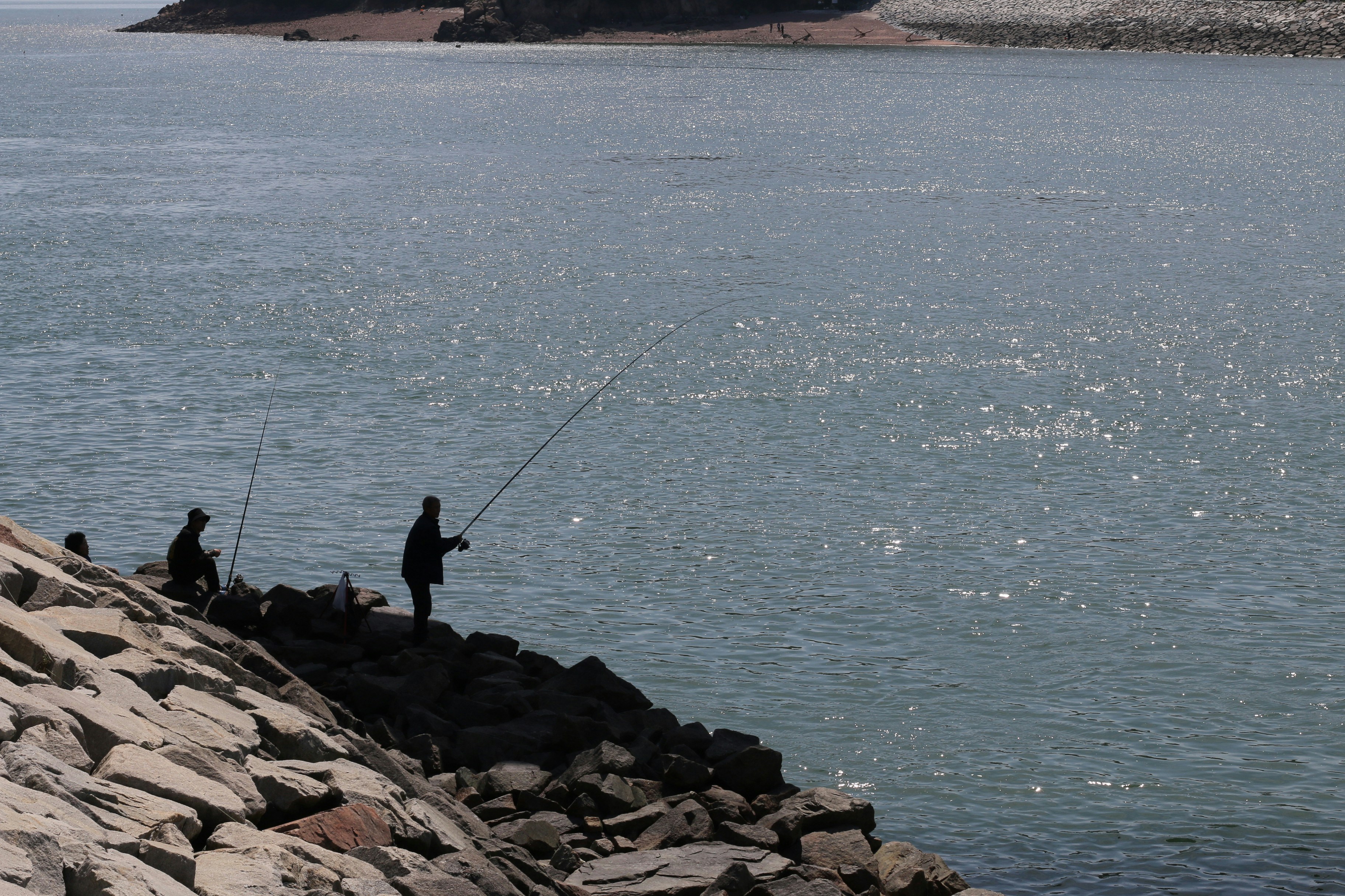 Line in the Water: Anglers Casting Silhouettes From the Pebbled Breakwater