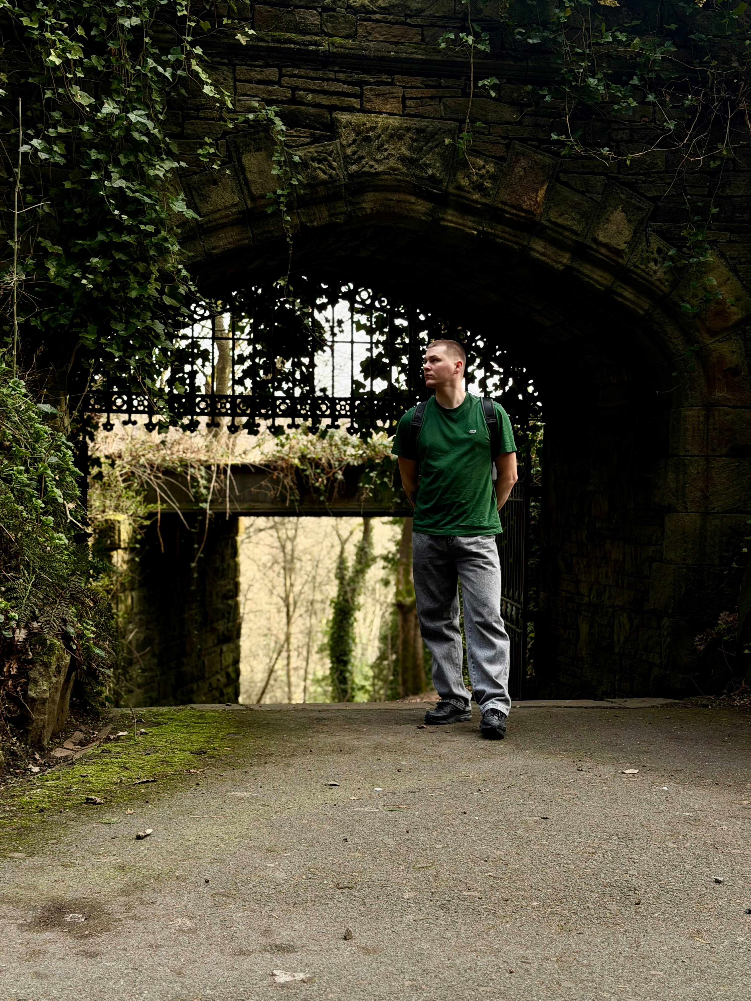 Man in Green T‑shirt Stands Under a Stone Arch, Surrounded by Ivy