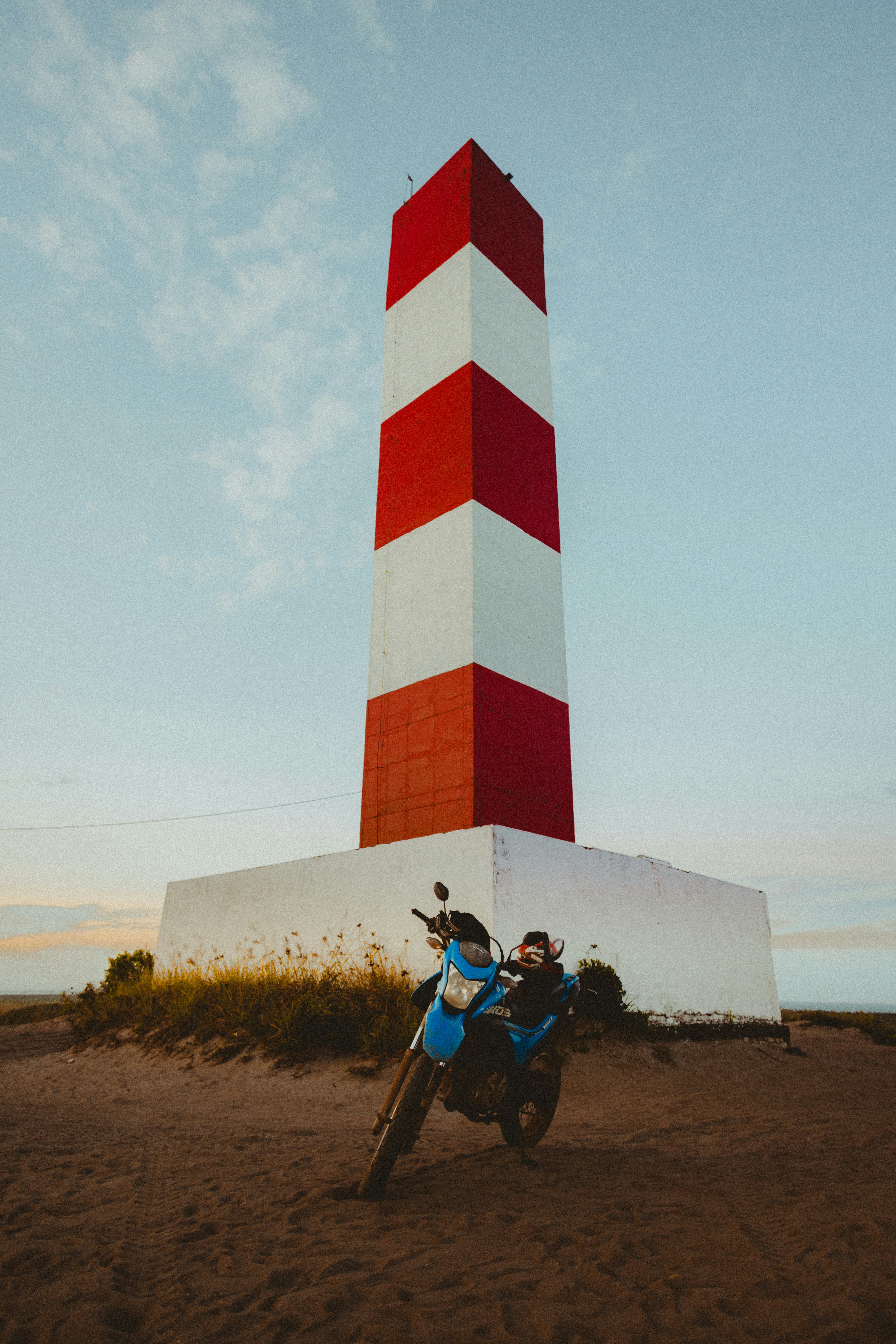 Stripes and Sand: A Red-and-White Beacon Beside a Shrouded Motorcycle