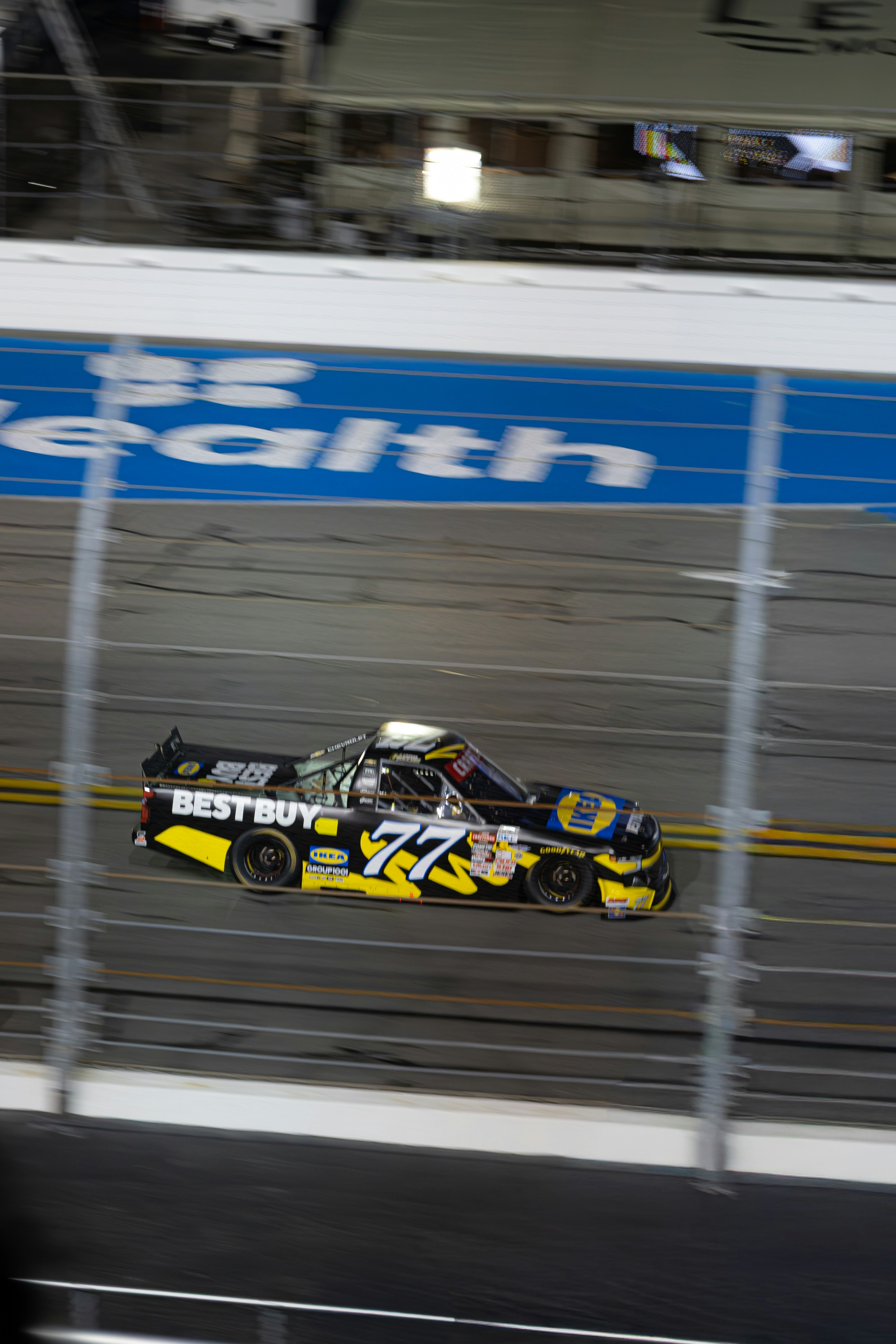 Yellow and black race truck blasts past a track fence in motion blur