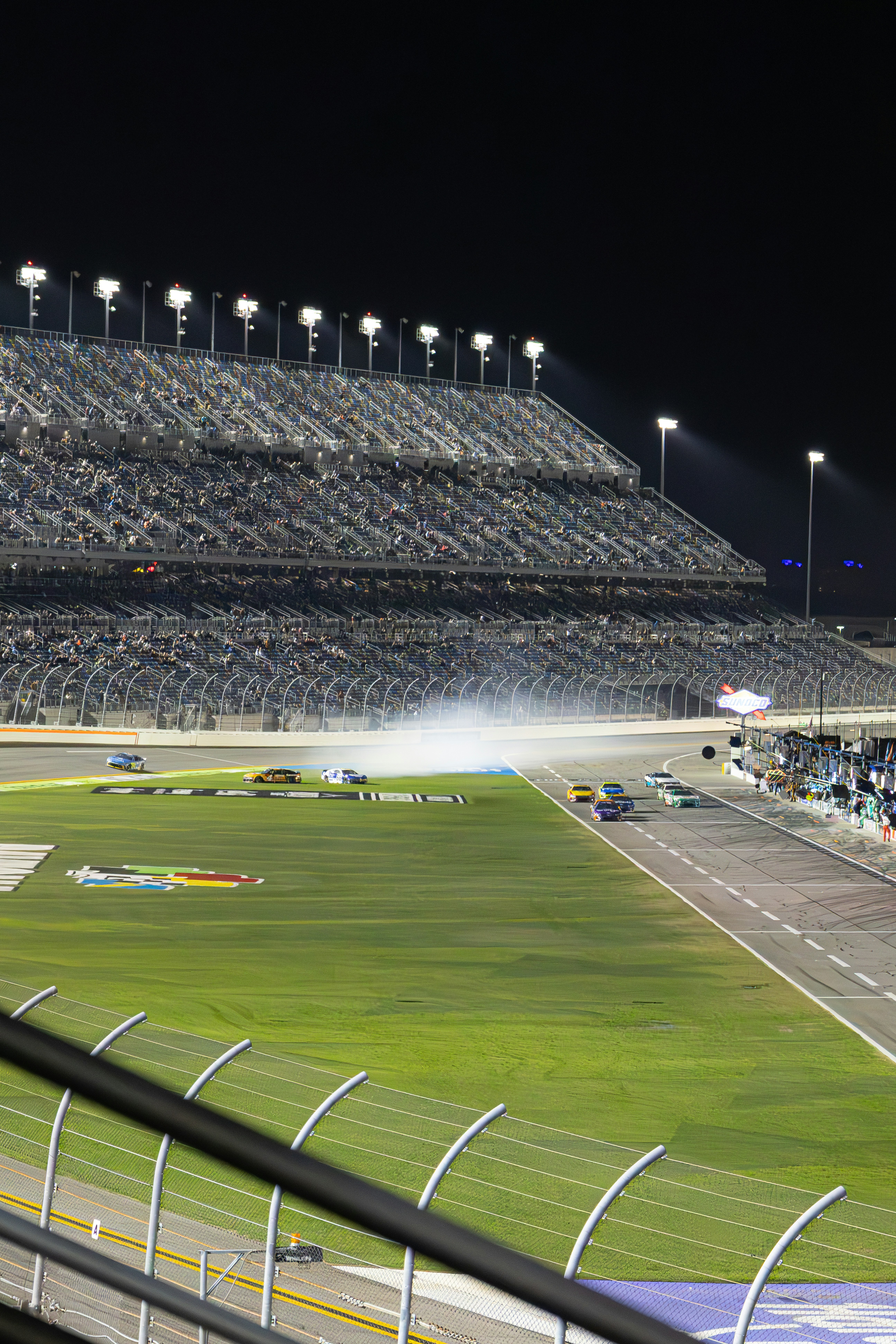 Night Sprint: Neon Lights, Fenced Track, and a Stadium of Rushing Cars