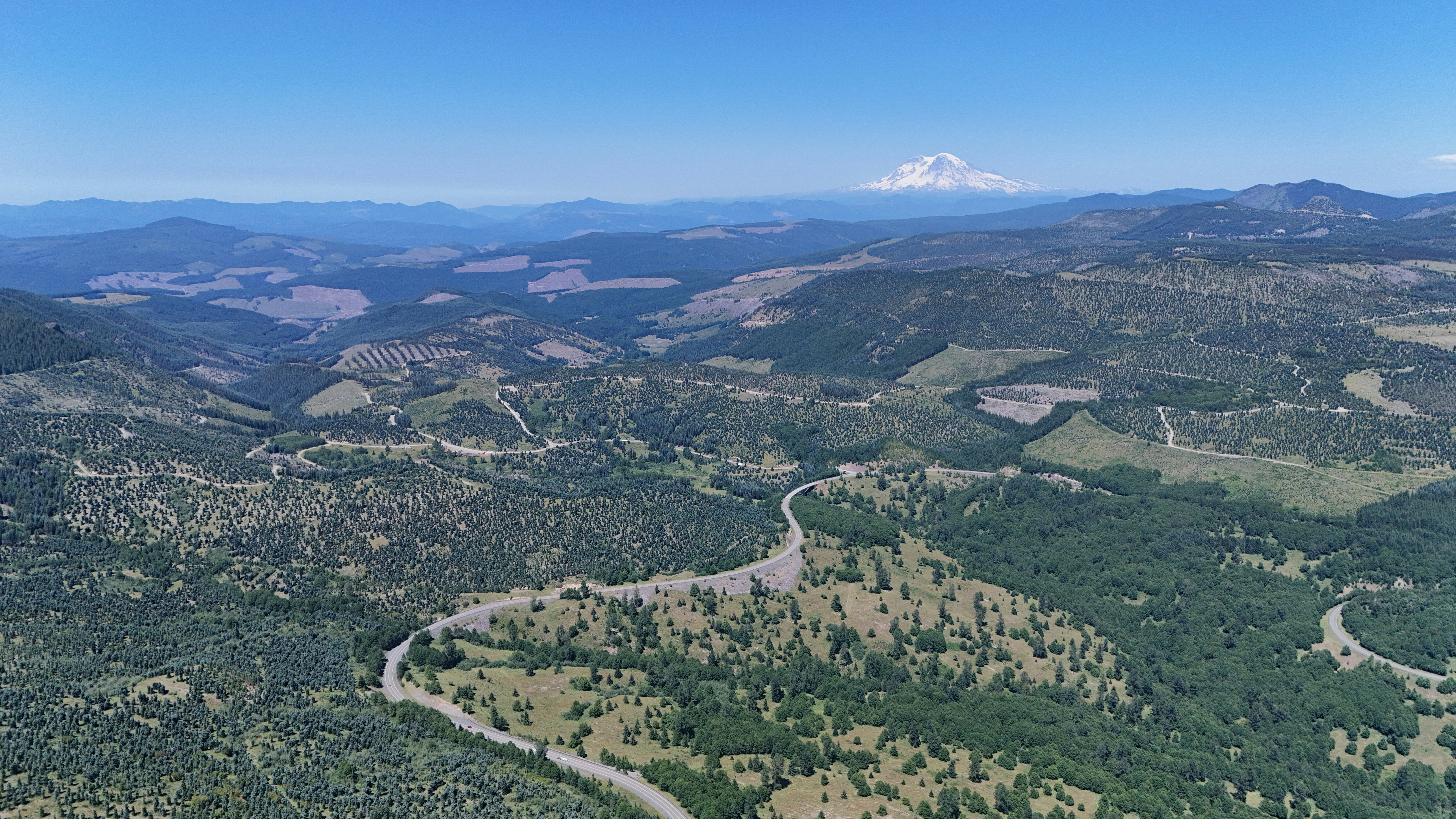 Aerial Run of the Cascades: Winding Roads Through Green Valleys Beneath a Snow-Tipped Peak