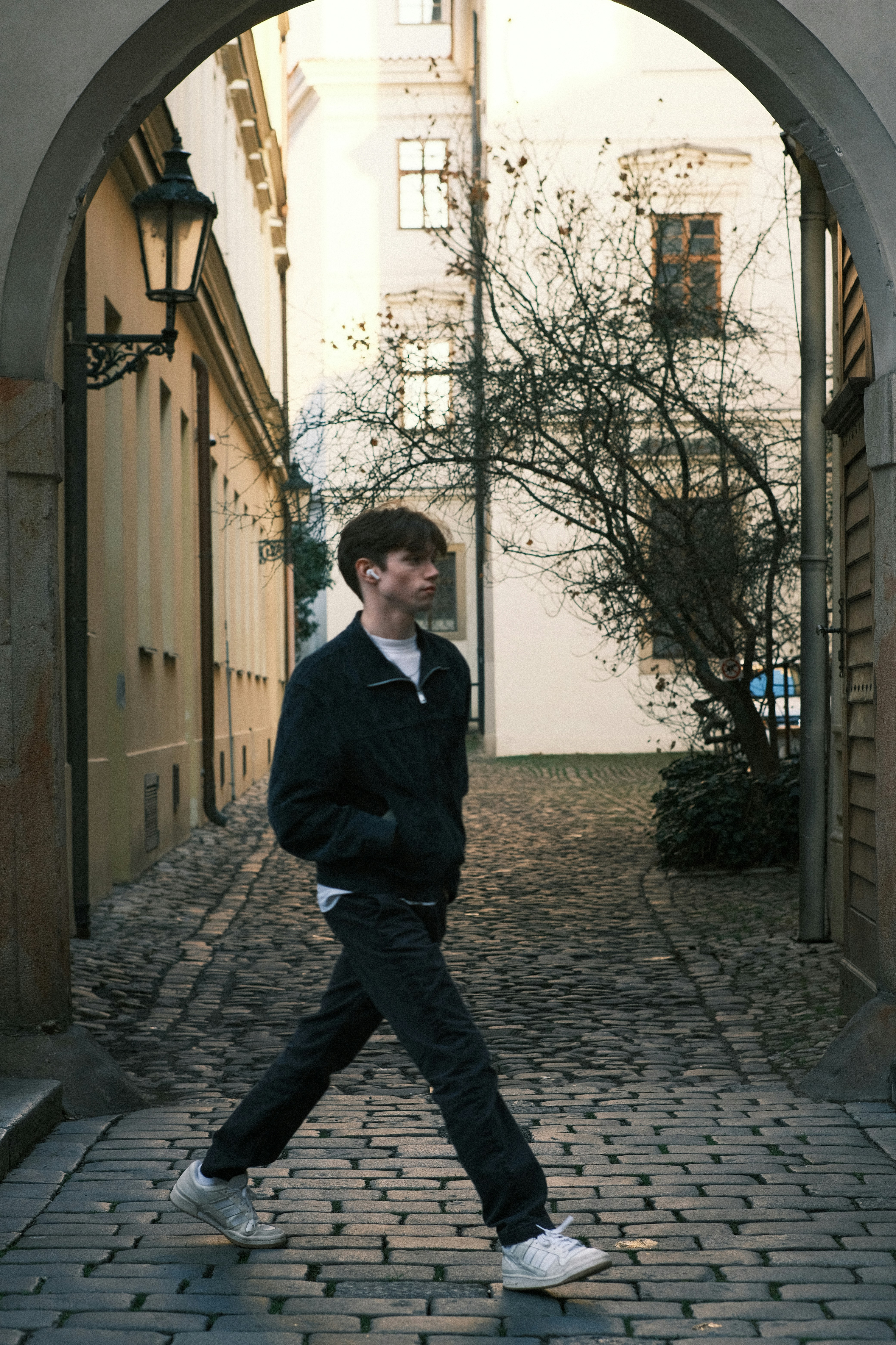 Stride Through the Arch: A Quiet Moment in the Cobblestone Corridor