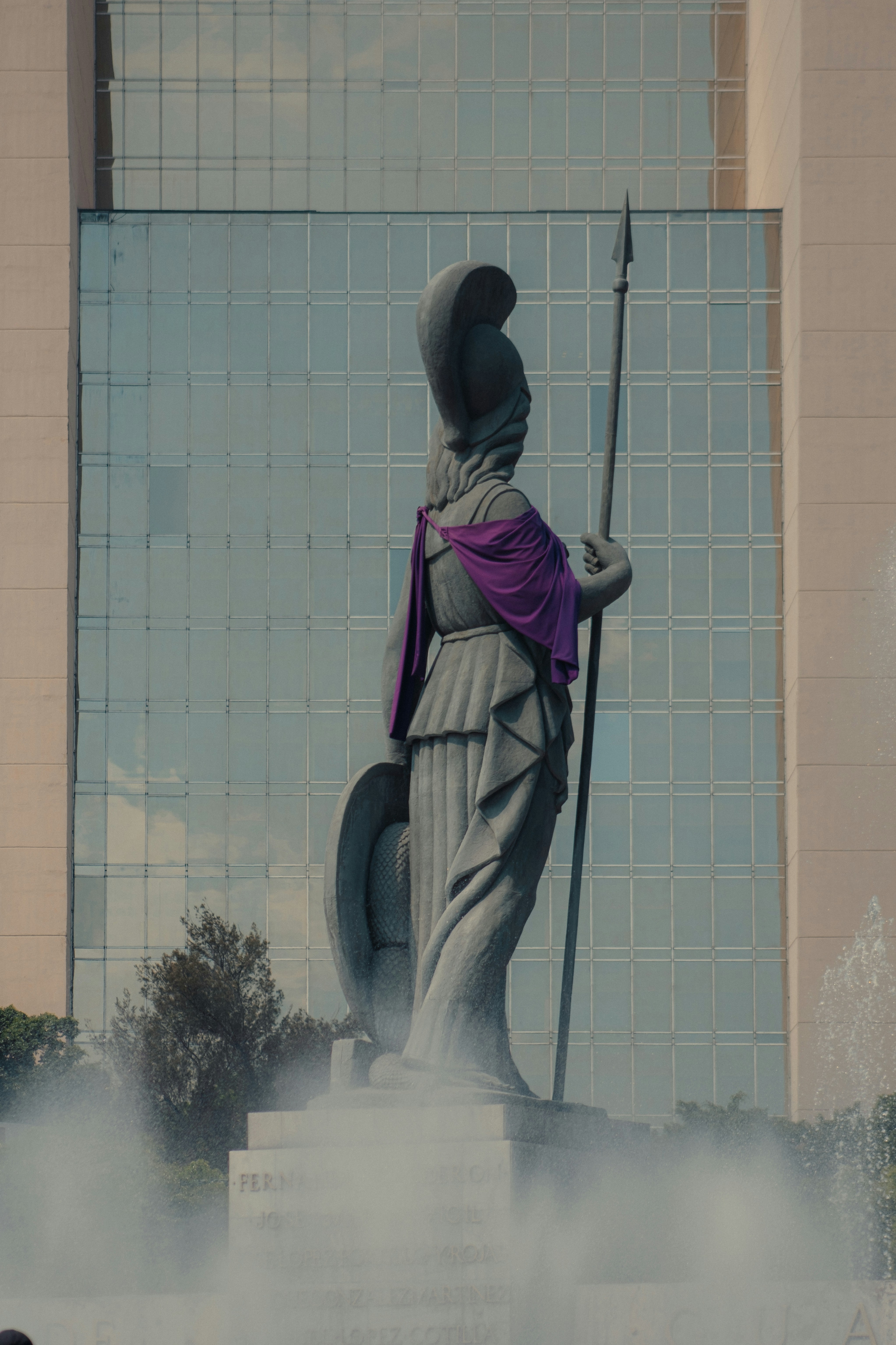 Guarded Grace: A statue in lavender drape before a glass tower