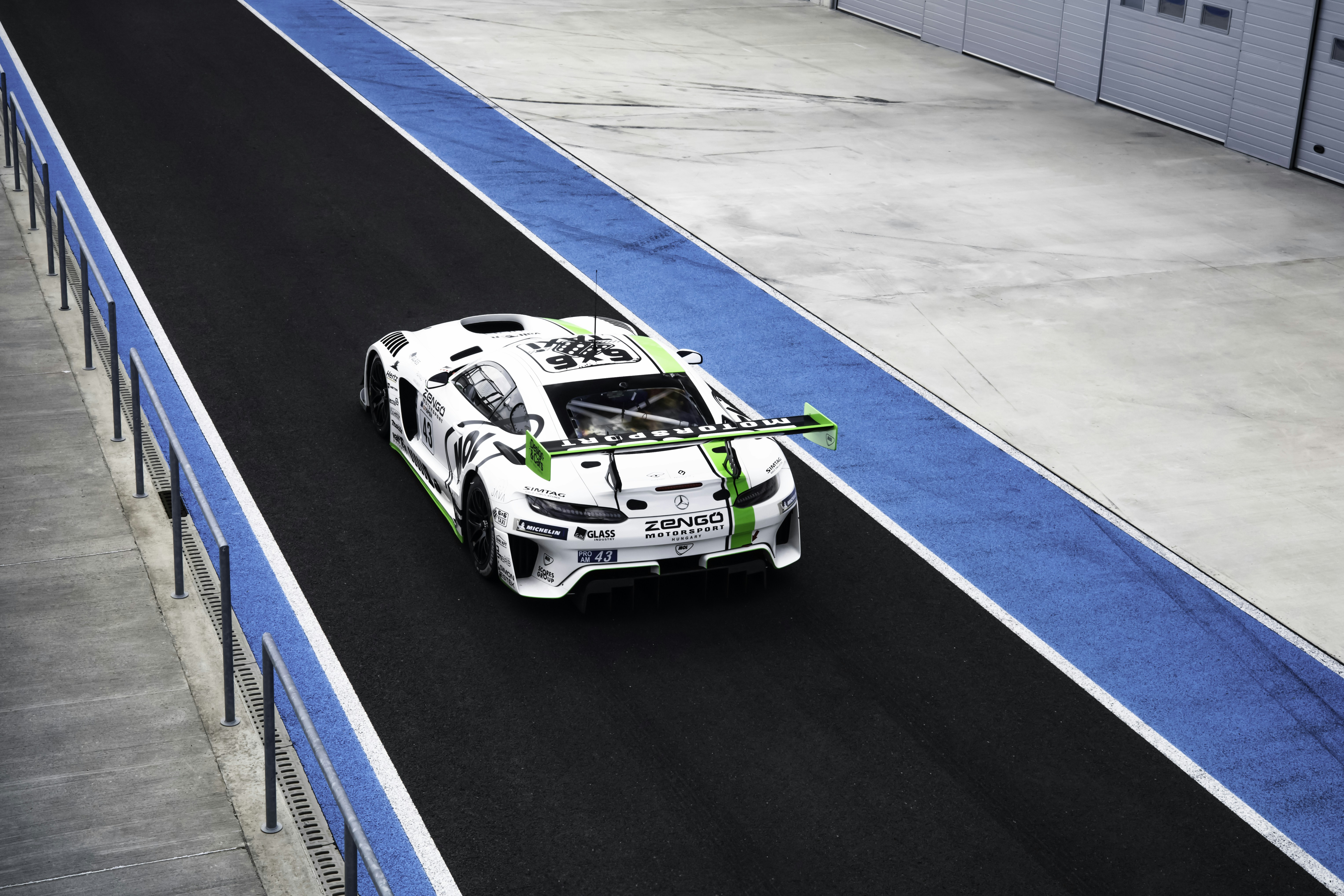 White race car on a blue-lined pit lane, captured from an elevated angle